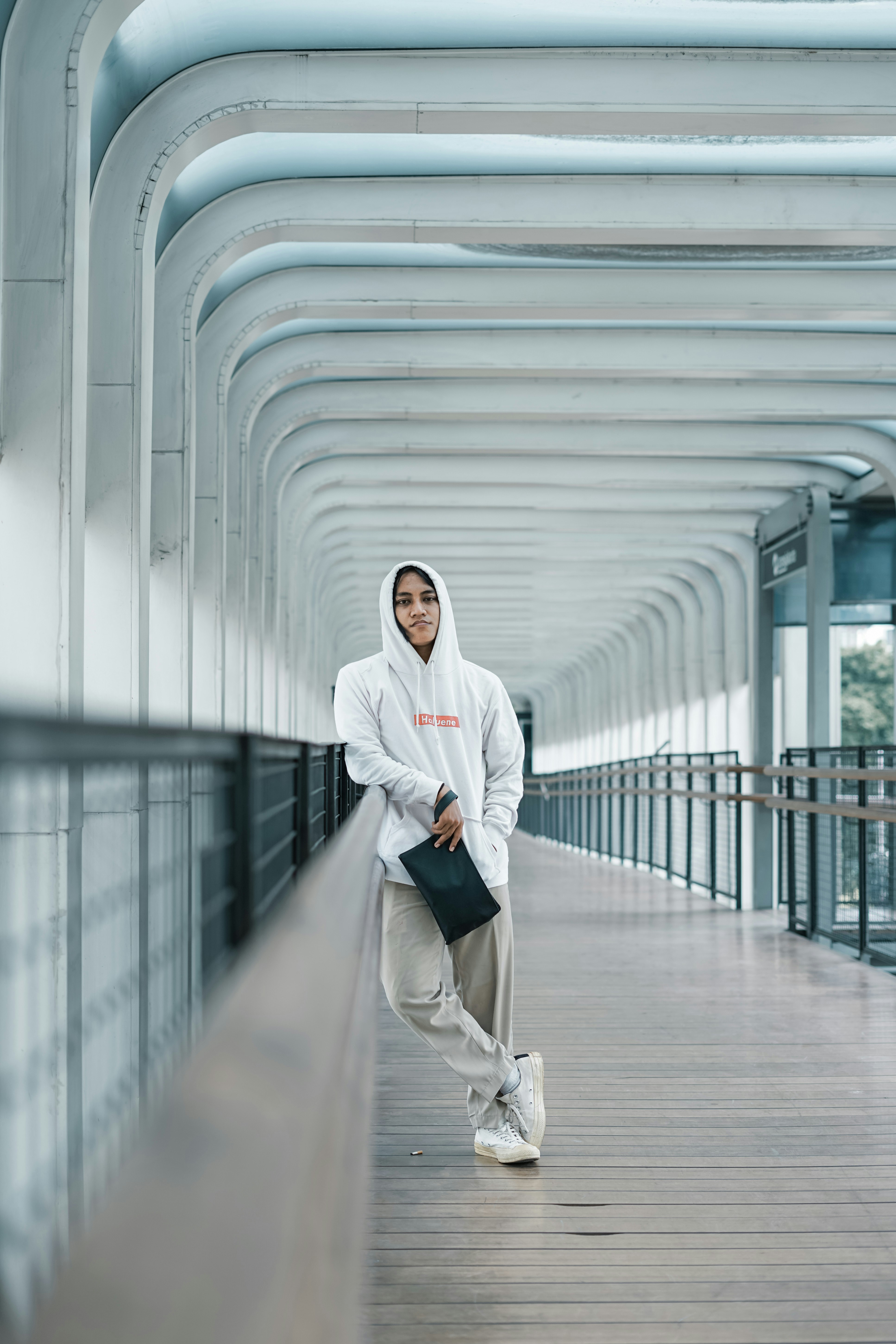 A young person in a white hoodie stands casually in a modern corridor, showcasing contemporary architecture and a relaxed urban vibe.