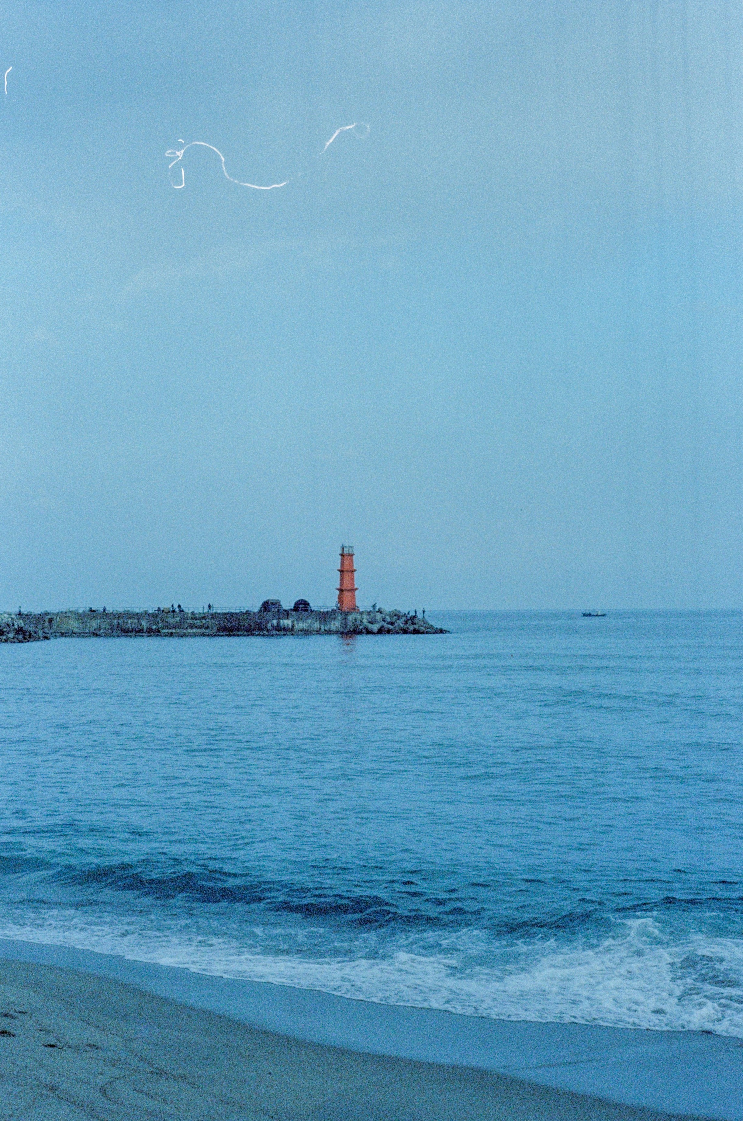 a red light house sitting on top of a beach next to the ocean