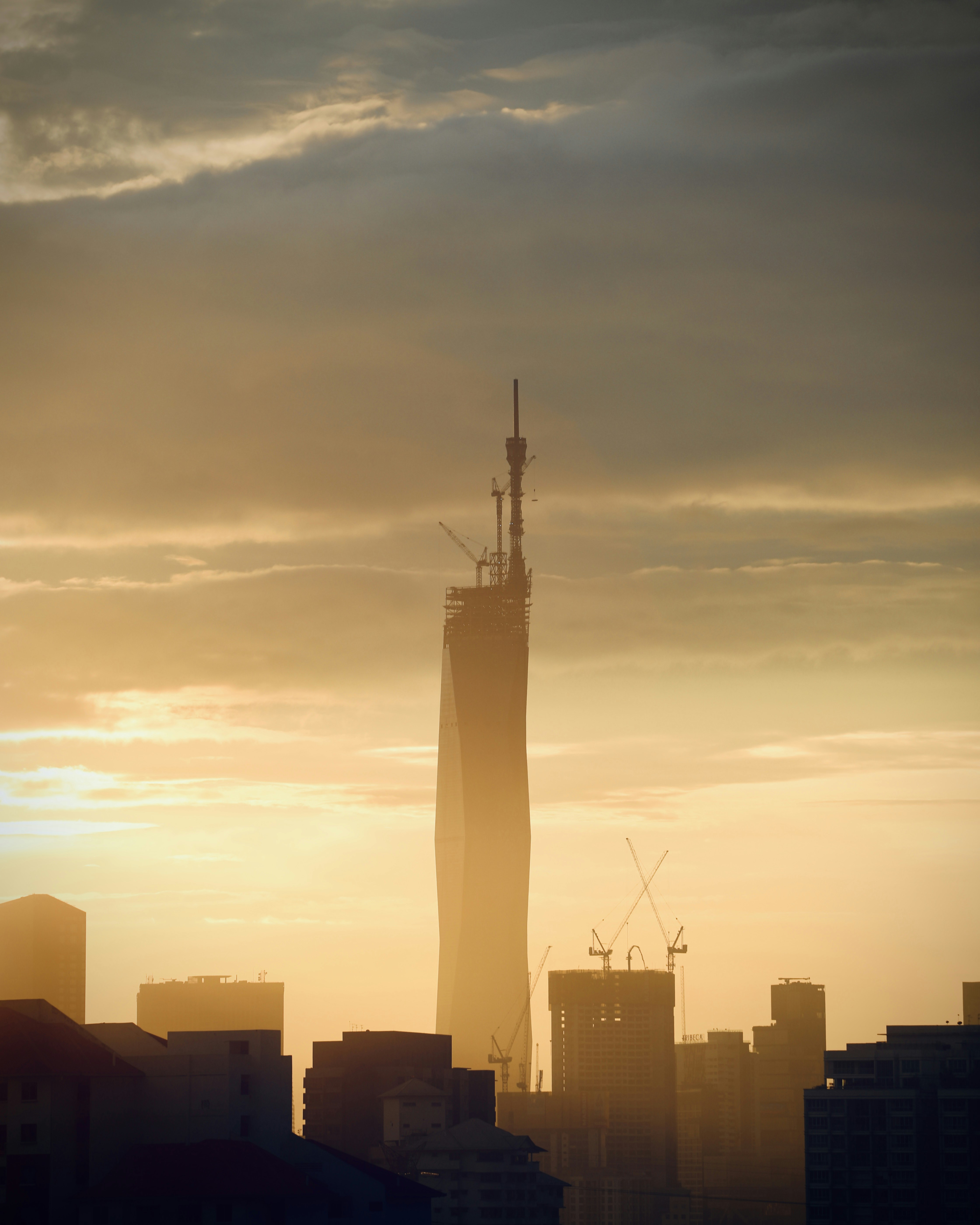 Golden Hour Apex: Crane-Crowned Tower Rising Over a Hazy City