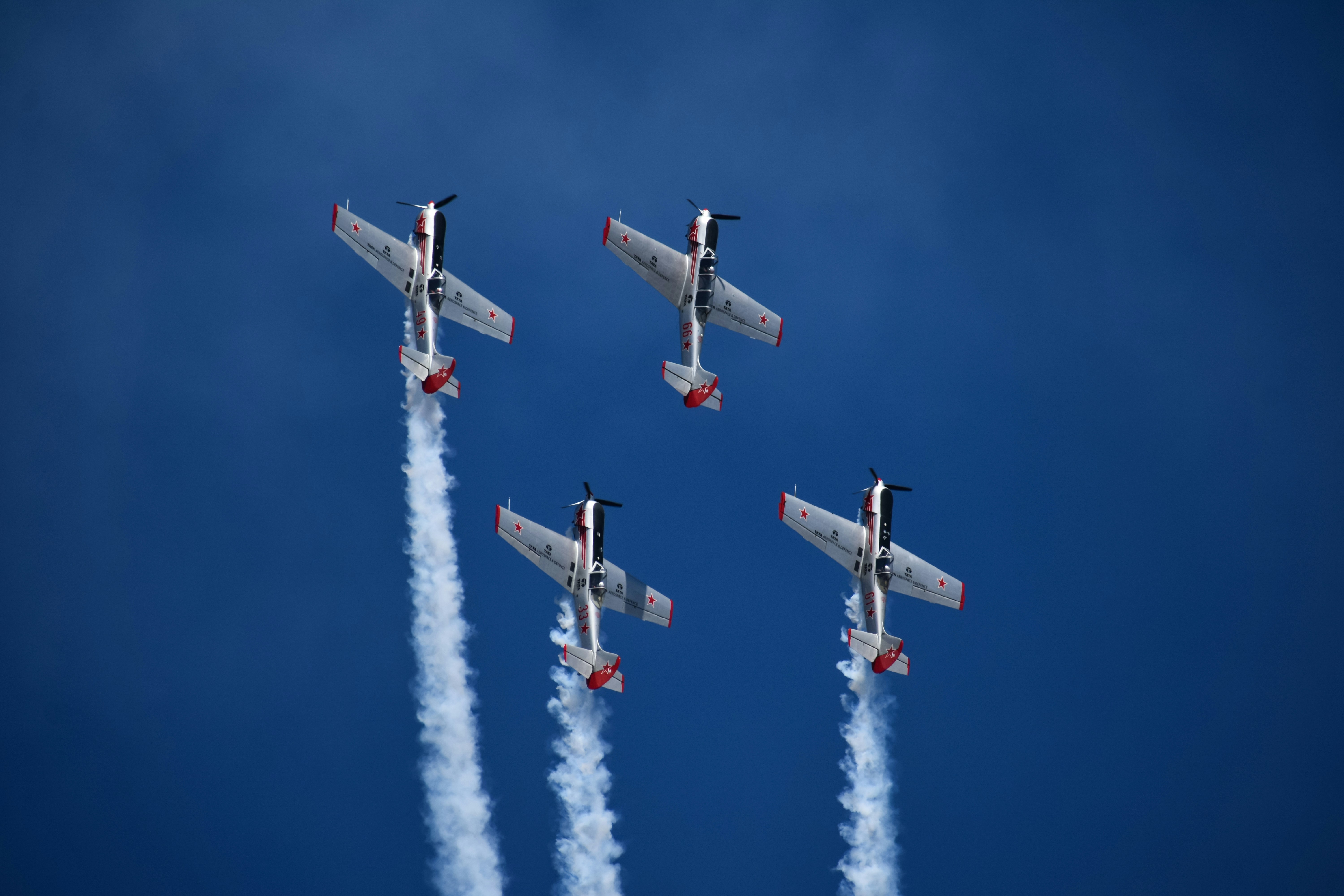 Four aircraft performing synchronized maneuvers against a clear blue sky, leaving trails of smoke behind them.