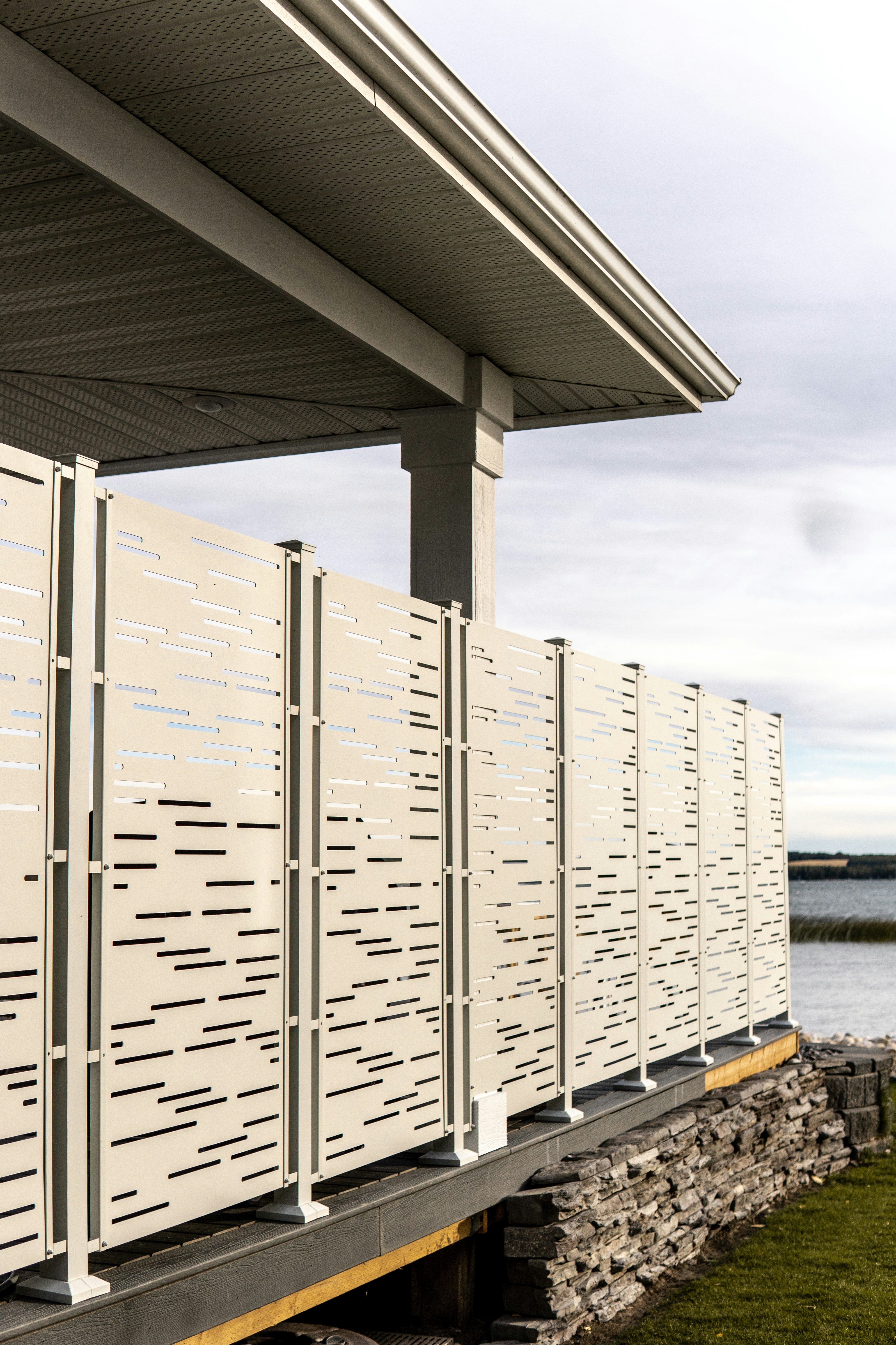 Stylish privacy screen with geometric patterns alongside a contemporary waterfront structure. The design blends seamlessly with the natural surroundings.