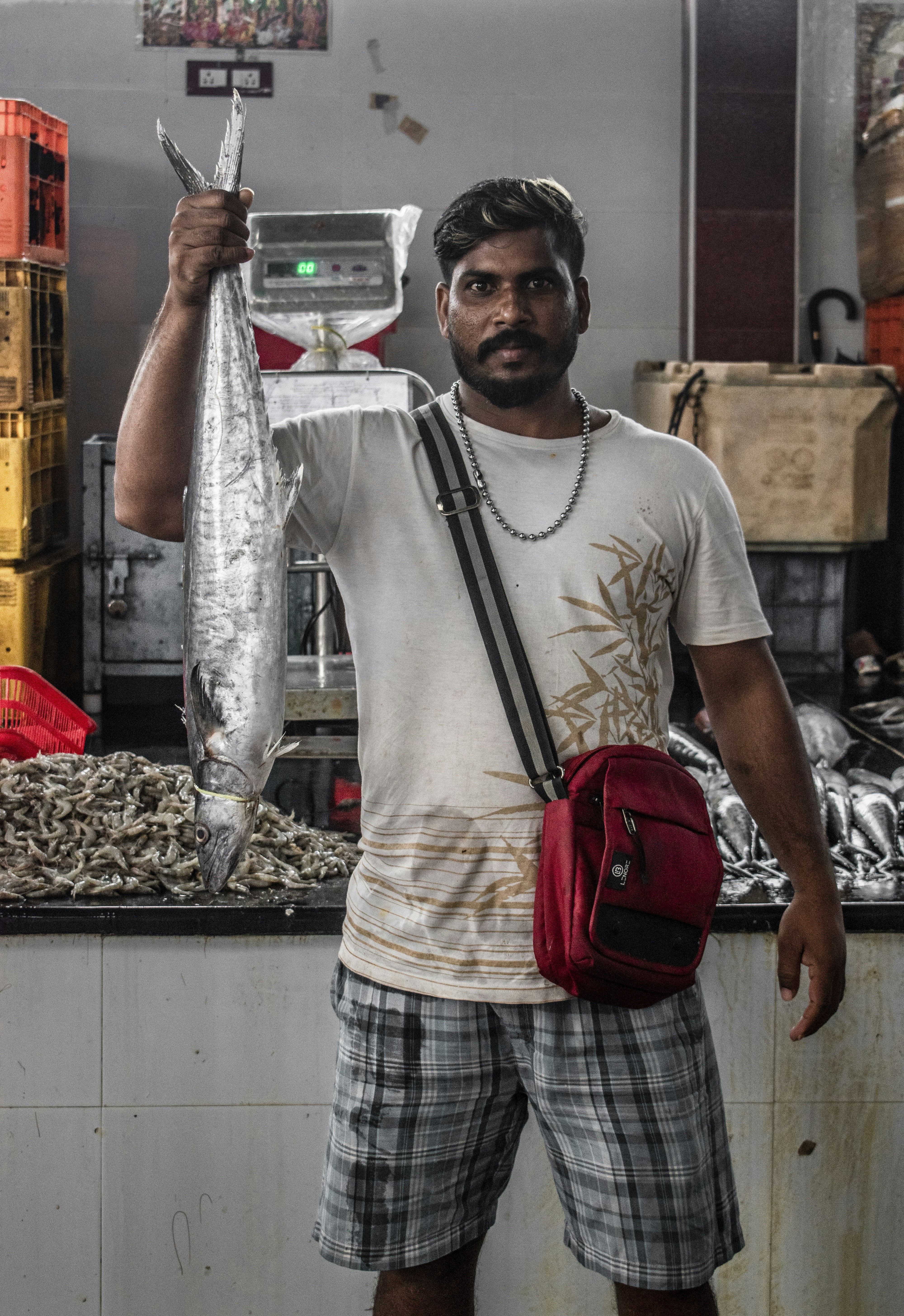 A man proudly holds a large fish in a bustling market surrounded by seafood. The scene captures the essence of daily life and trade.
