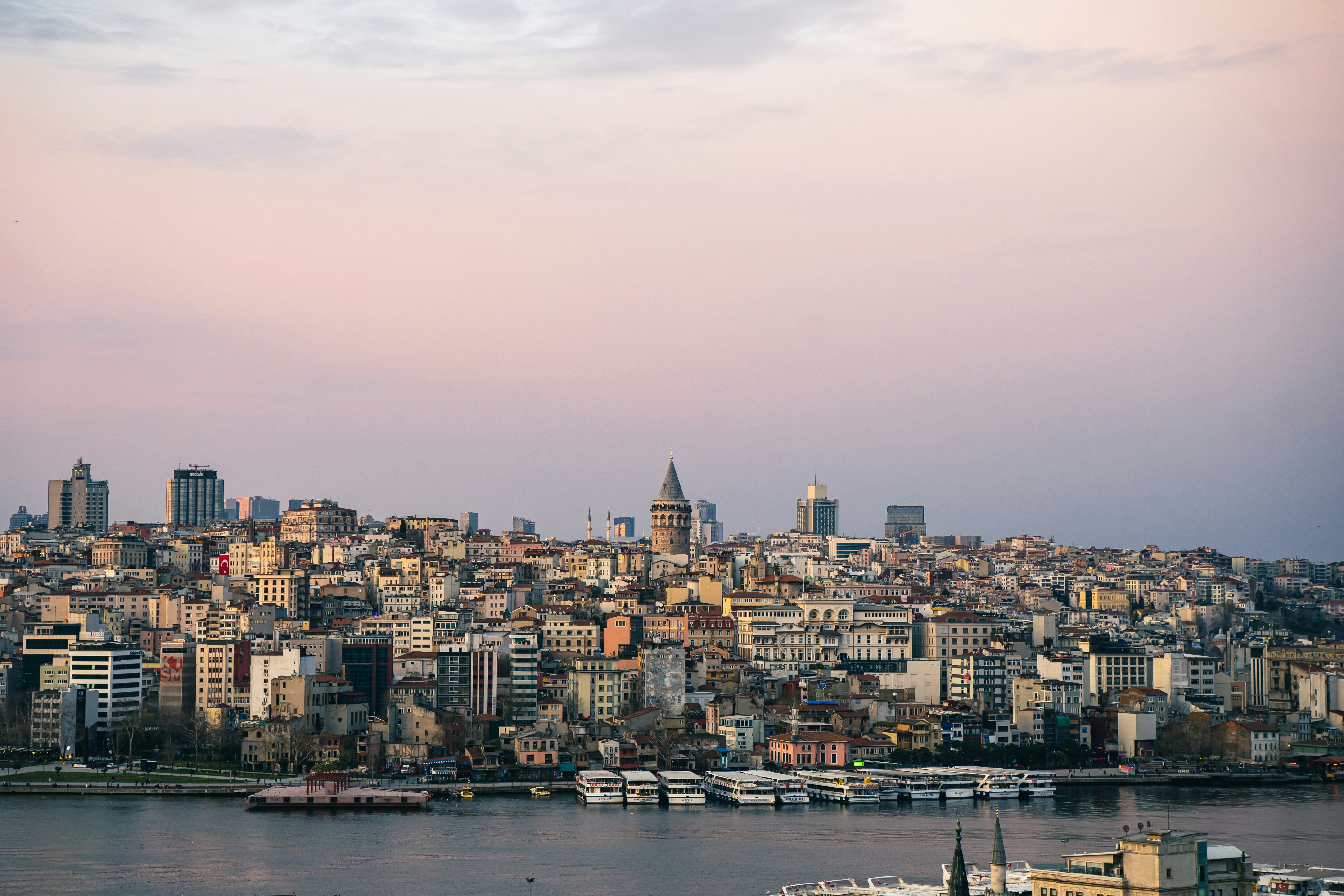 A panoramic view of Istanbul's skyline at dusk, showcasing the historic Galata Tower amidst a sea of modern buildings along the waterfront.