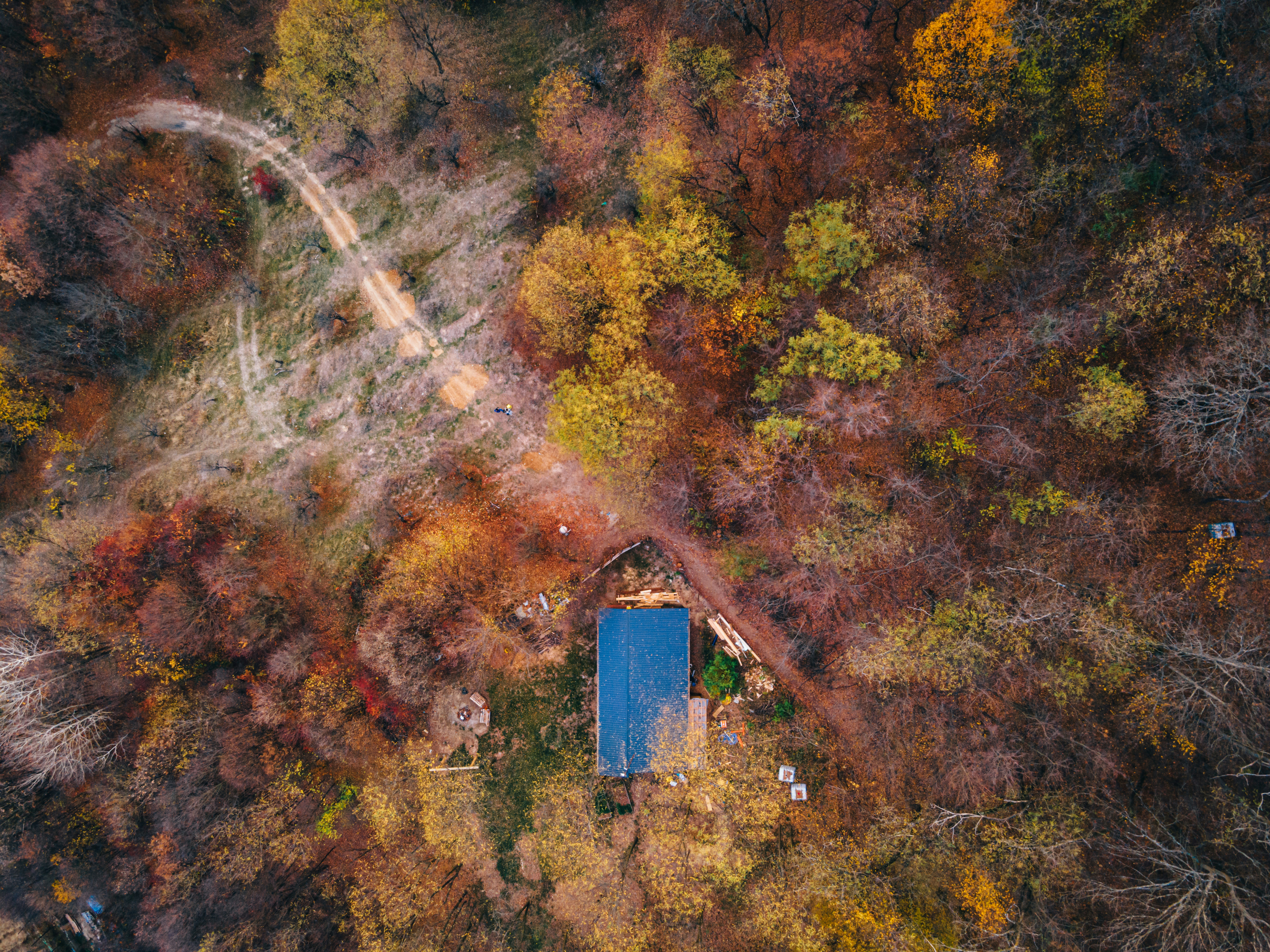 Aerial view of a secluded cabin surrounded by vibrant fall foliage, showcasing the rich tapestry of autumn colors. The winding path leads toward the tranquil retreat.