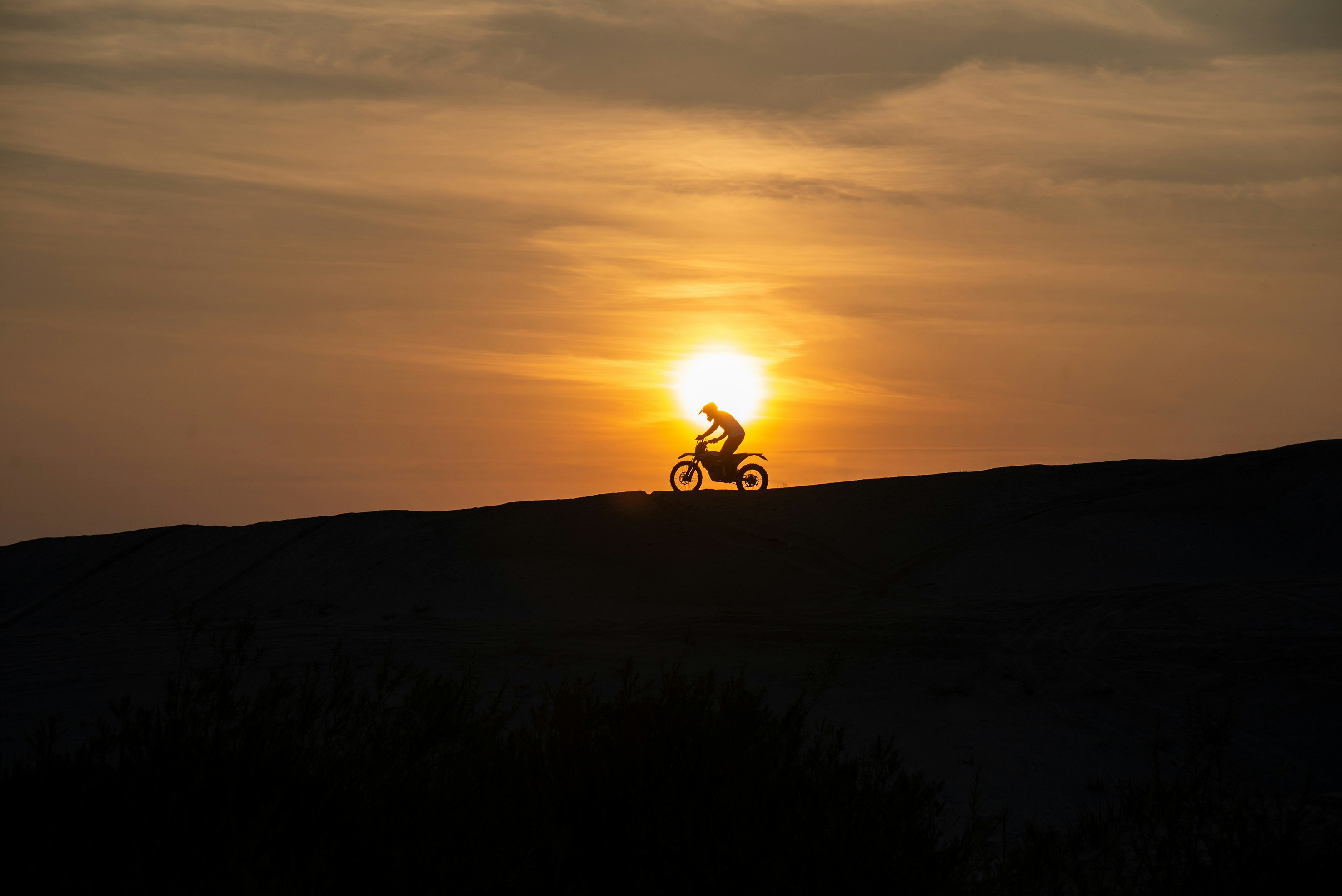 Dune Silhouette at Sunset: A Solitary Cyclist Traces a Quiet Arc