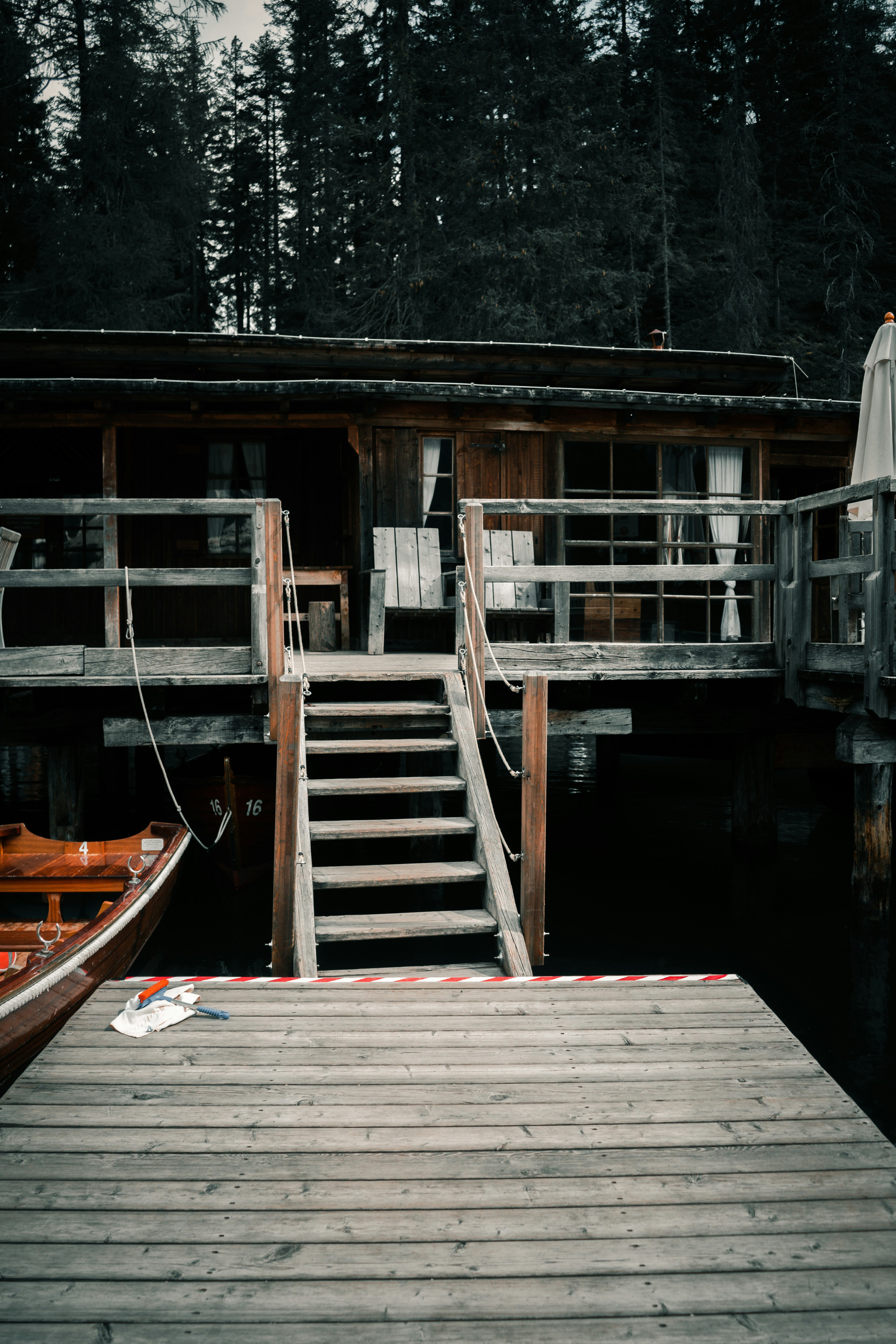 Wooden dock leading to a rustic cabin, framed by tall trees, with a small boat moored nearby. The tranquil scene evokes a sense of serenity.
