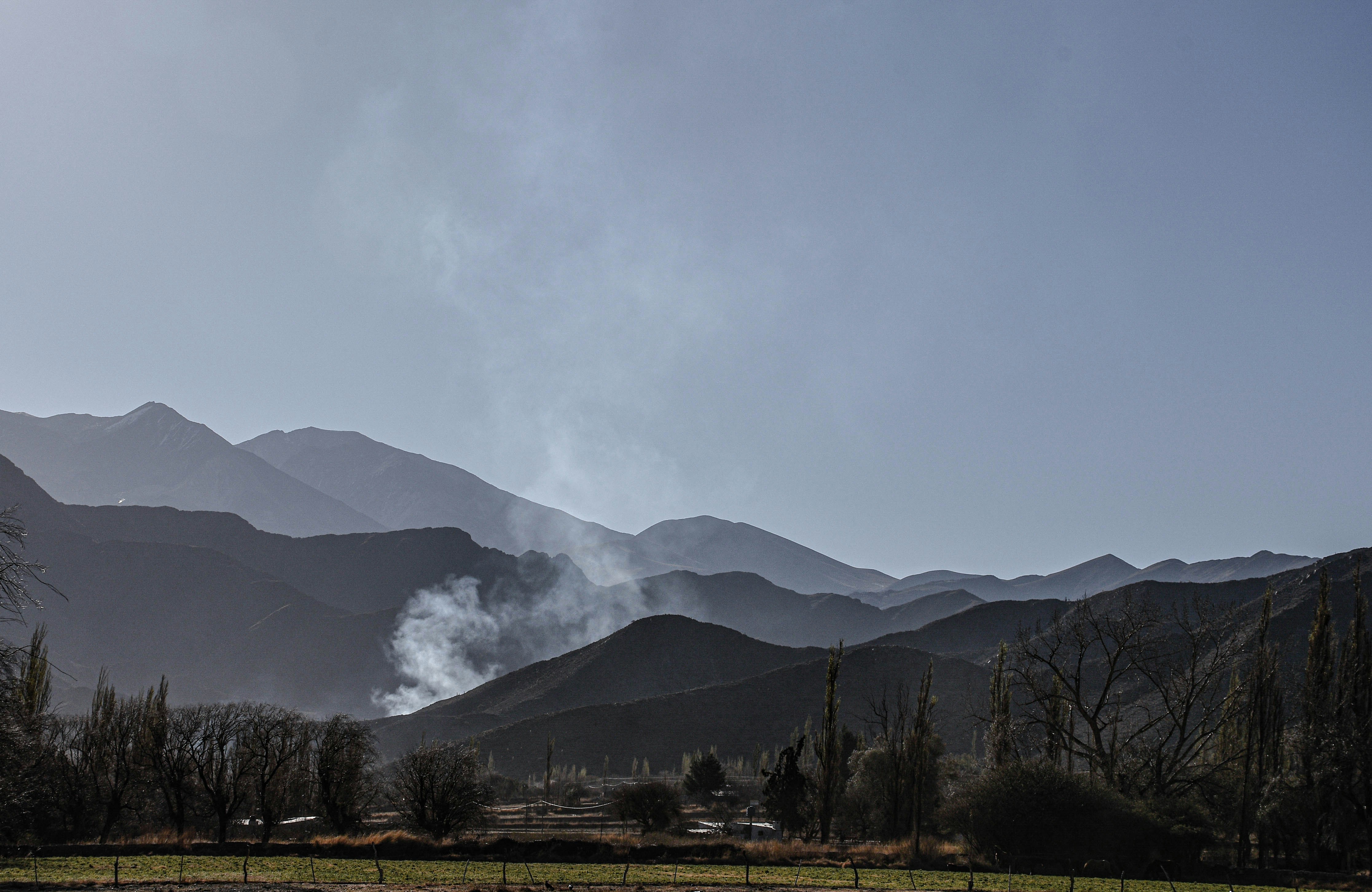 Smoke rises against a backdrop of layered mountain ridges under a clear sky.