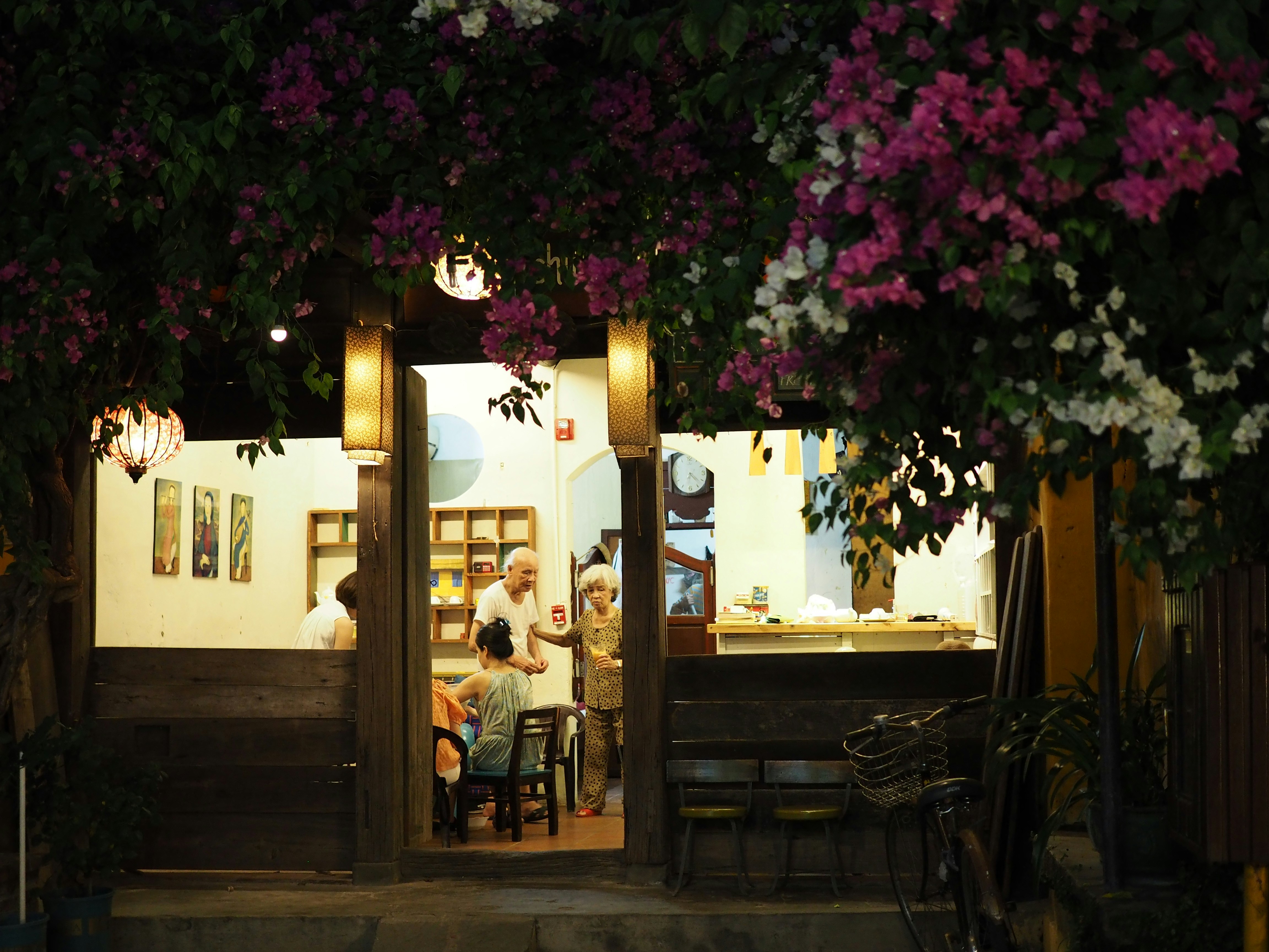 Cozy restaurant entrance framed by vibrant bougainvillea, revealing diners enjoying a lively atmosphere inside.
