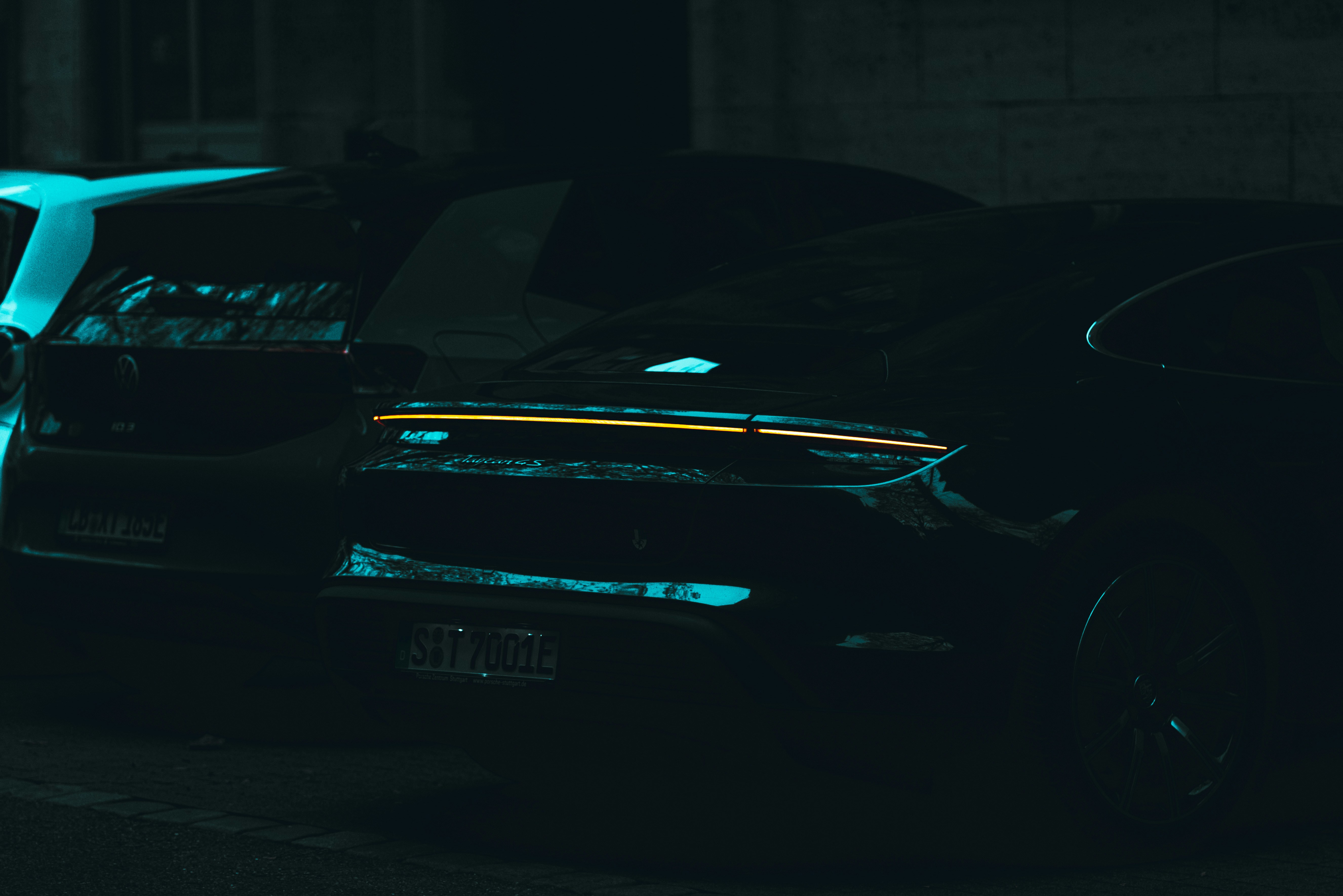 Three parked cars in a dimly lit urban setting, highlighting the sleek rear design of a luxury vehicle illuminated by subtle neon accents.