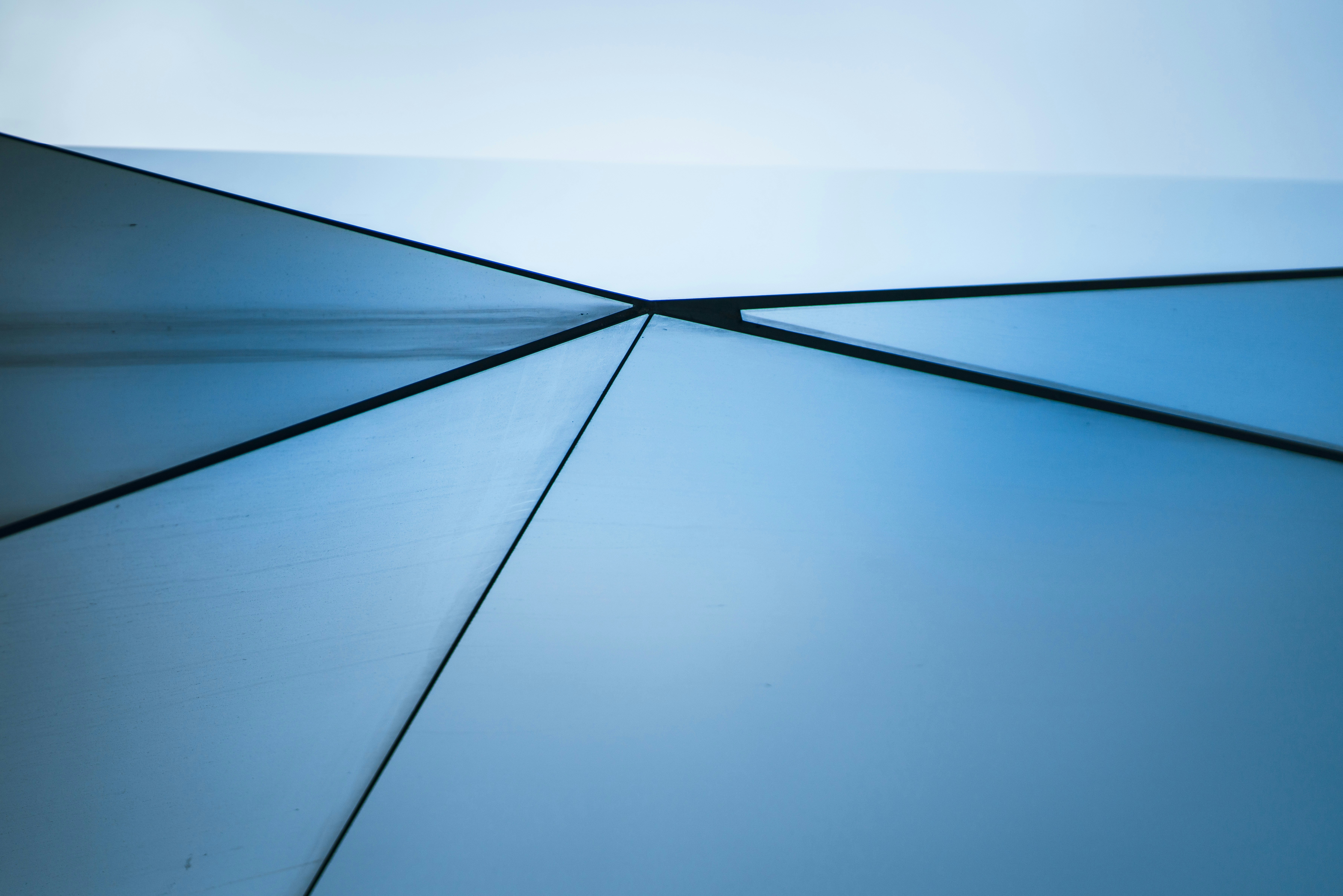 Abstract composition of intersecting glass panels reflecting soft blue tones. The angles create a dynamic interplay of light and shadow.