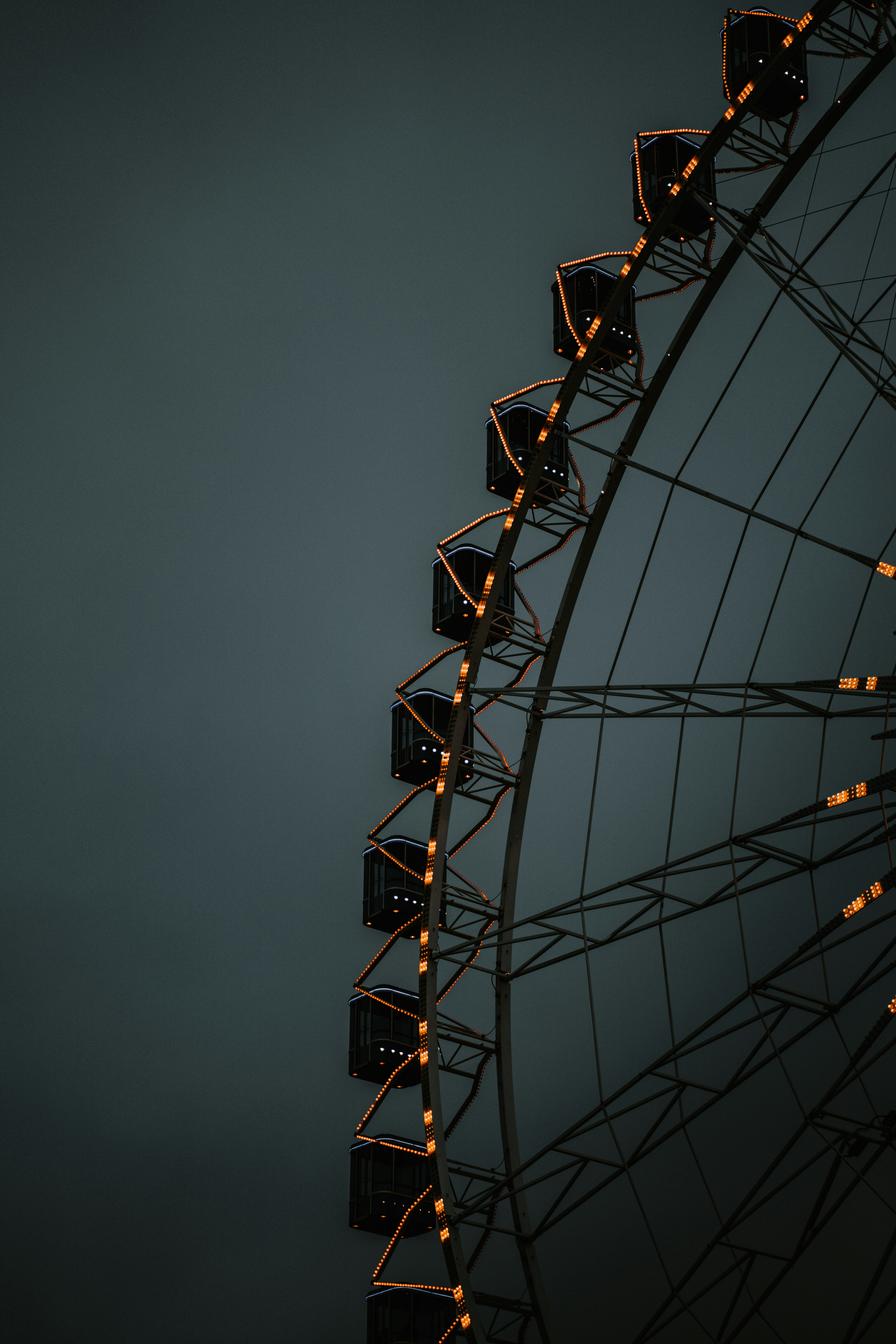 A close-up of a Ferris wheel's illuminated structure against a dark, moody sky.