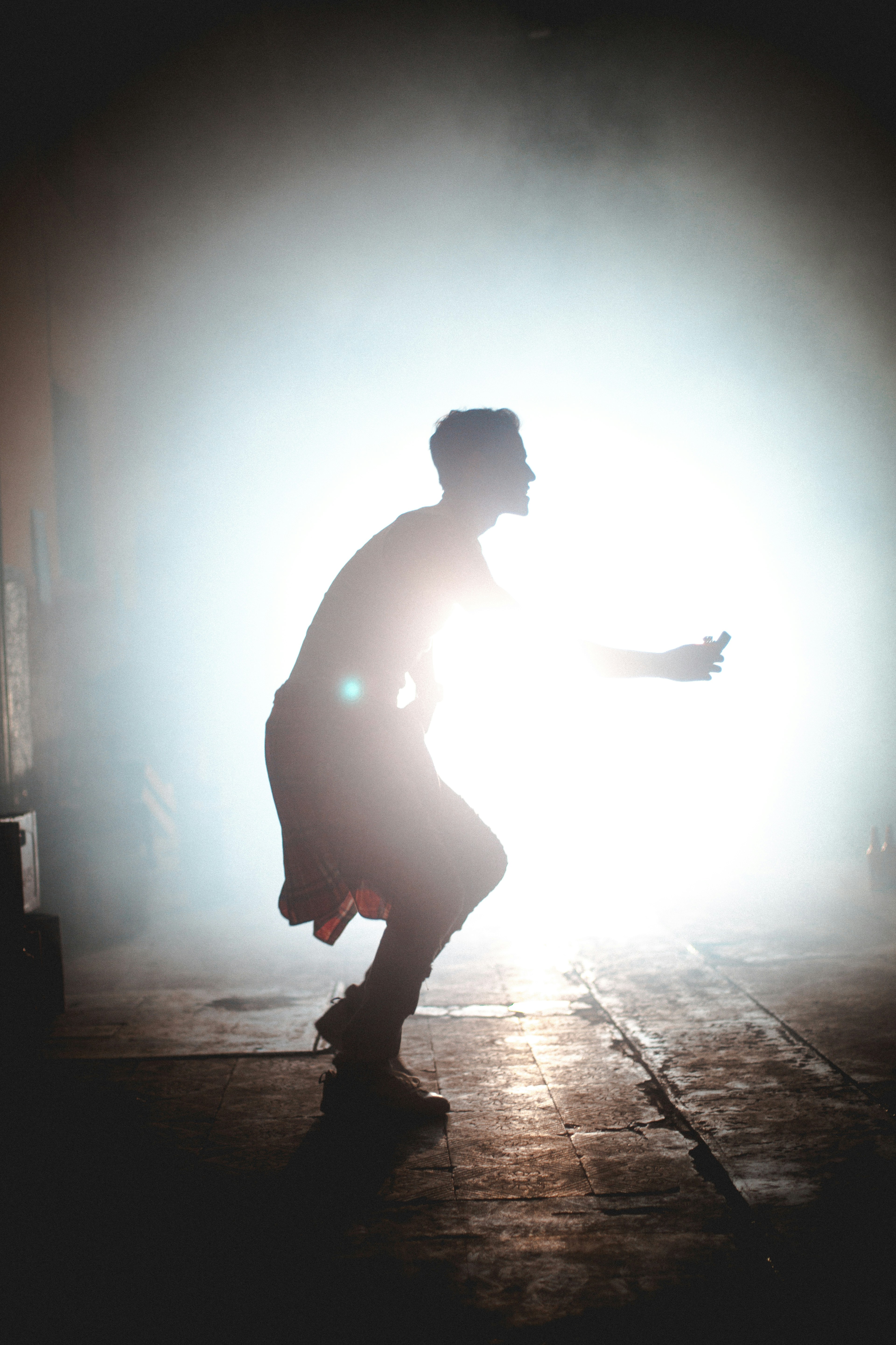 Silhouette of a dancer reaching towards a bright light amidst smoky surroundings.