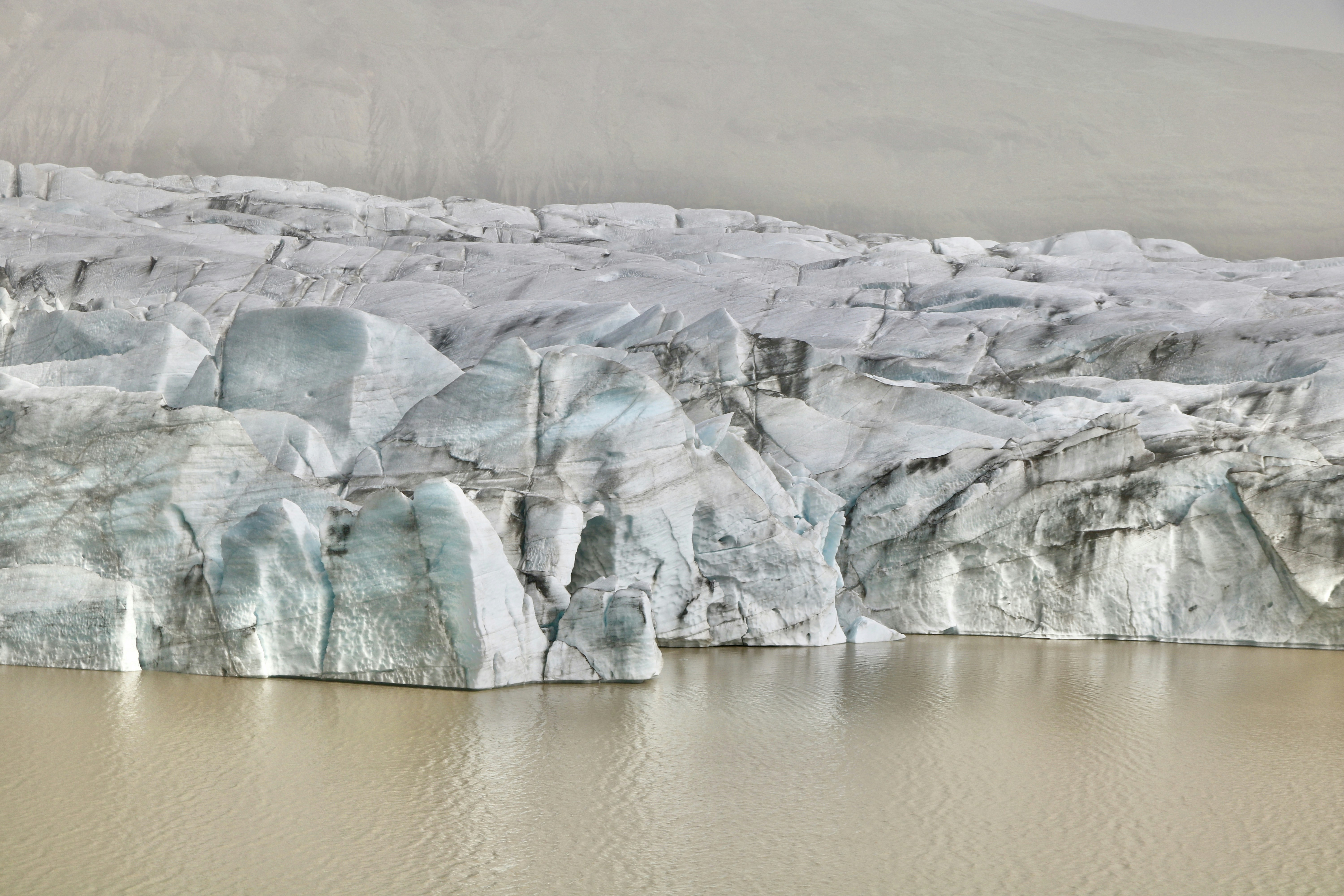 Glacial ice formations reflect subtle hues above a calm, muddy lake, illustrating the delicate balance of nature's elements.