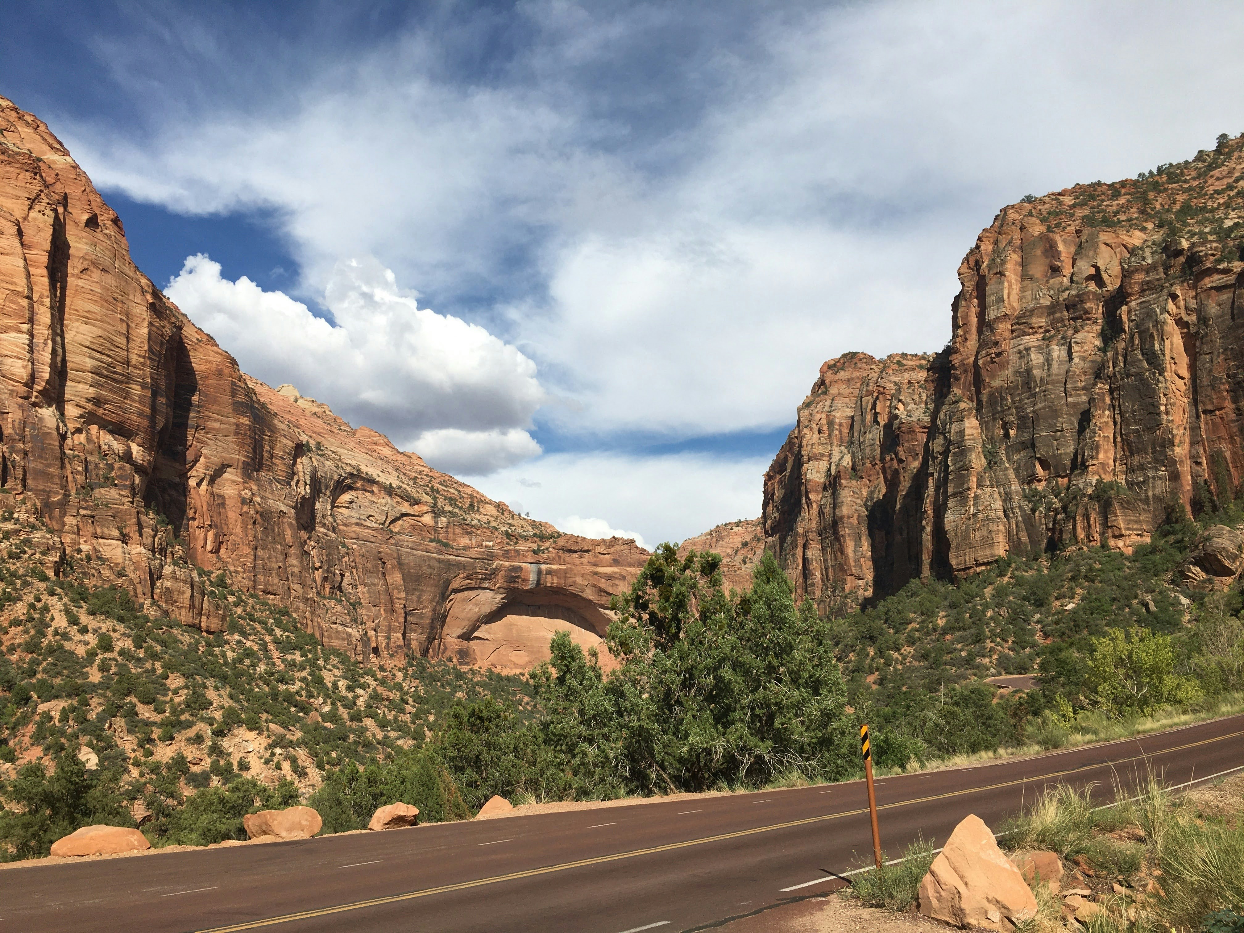 Winding road leading through towering red rock formations under a partly cloudy sky.