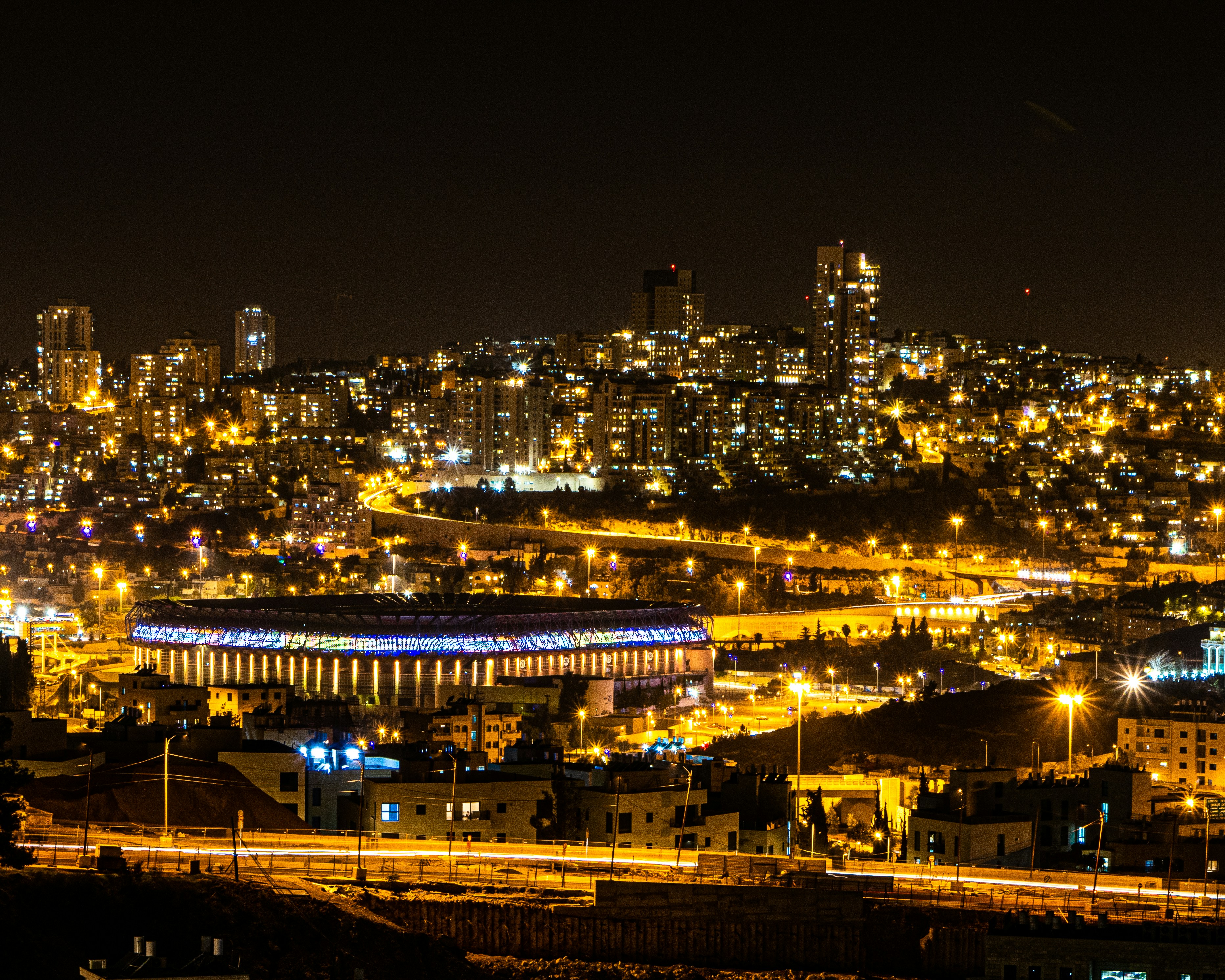 Illuminated stadium surrounded by a vibrant cityscape at night, showcasing a blend of architecture and urban life.