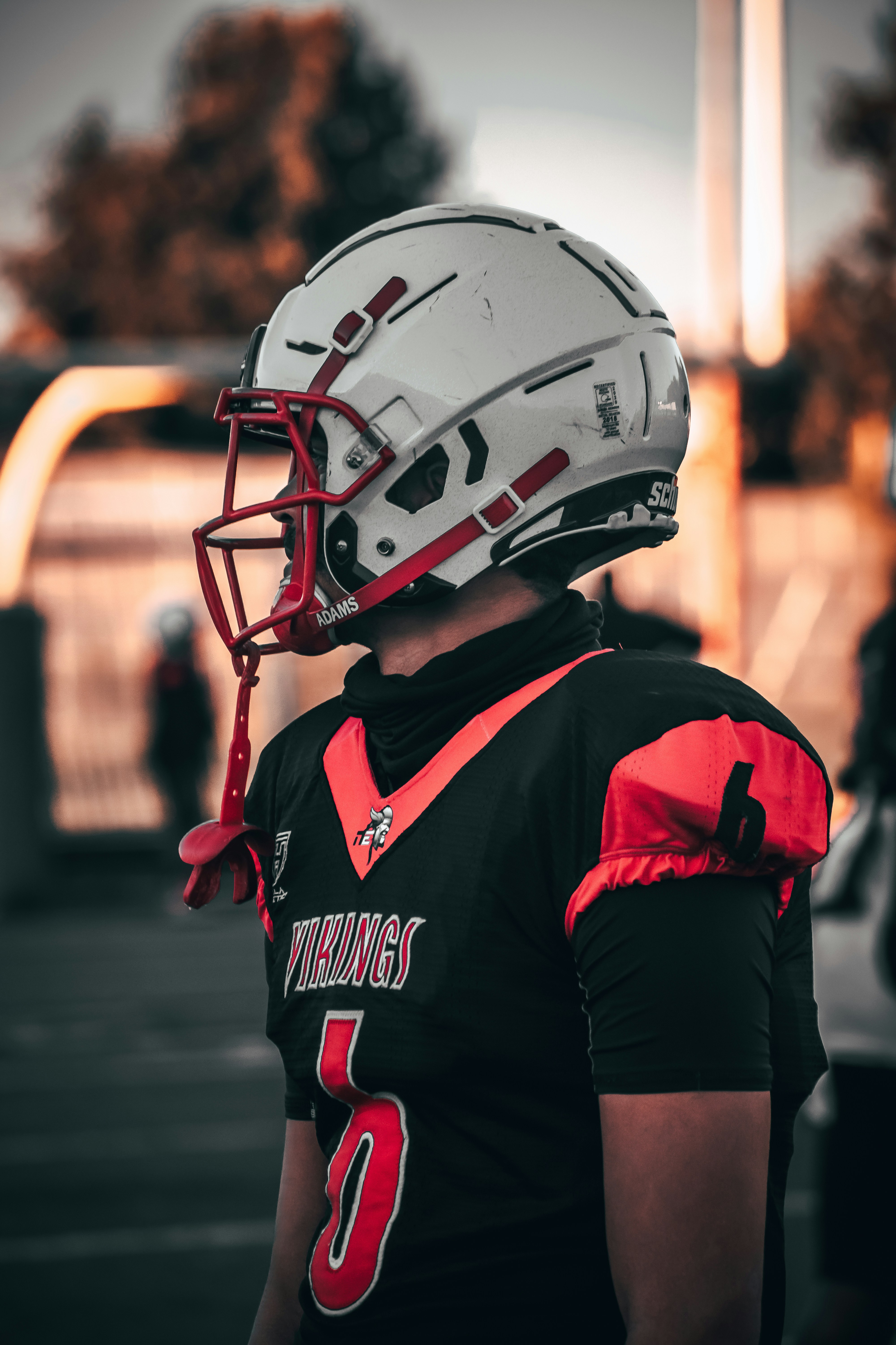 Football player in a black and red uniform looks on, helmet gleaming under stadium lights, ready for the game.