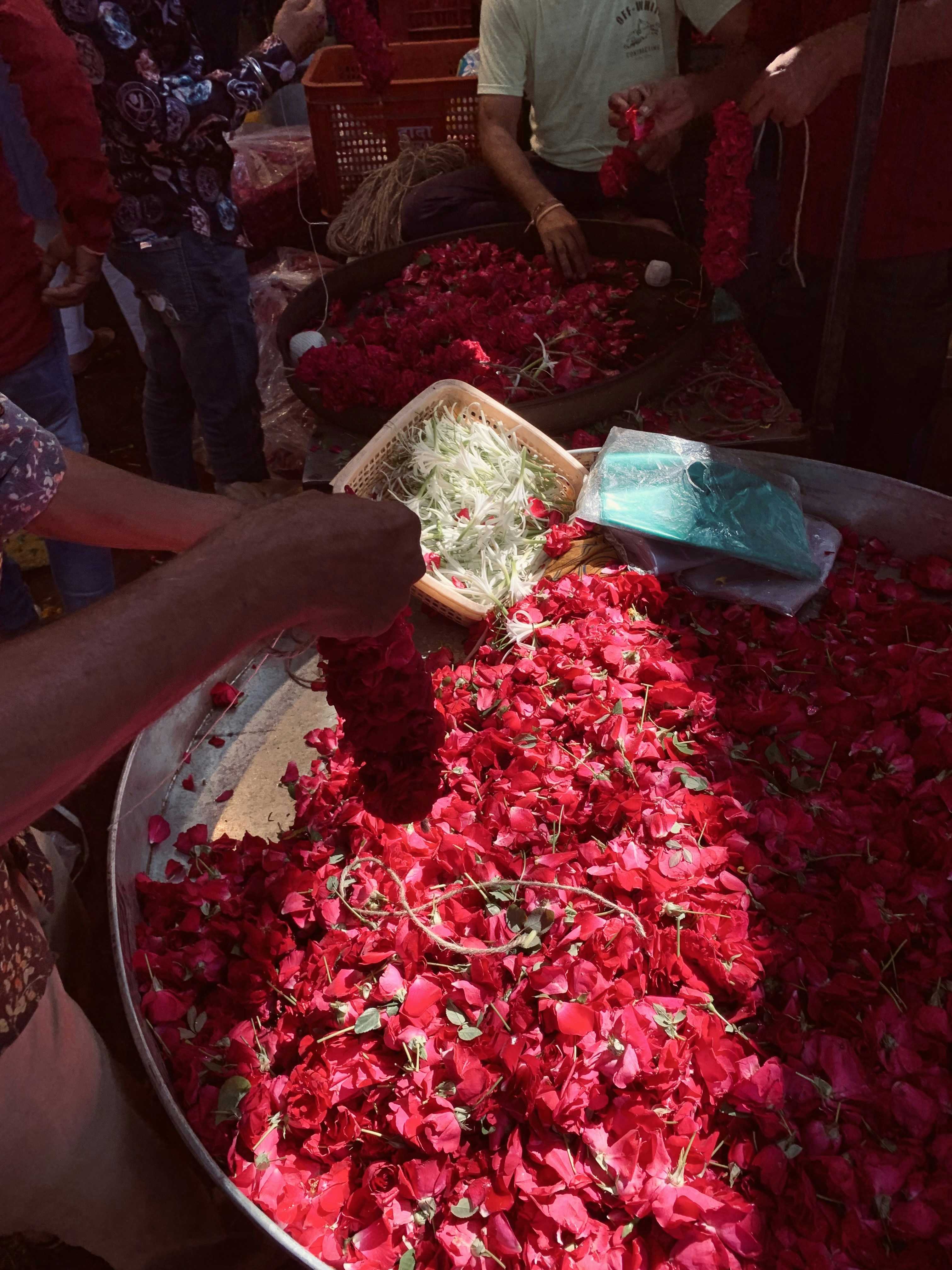 Hands skillfully assembling garlands from vibrant rose petals amidst a lively floral market scene.