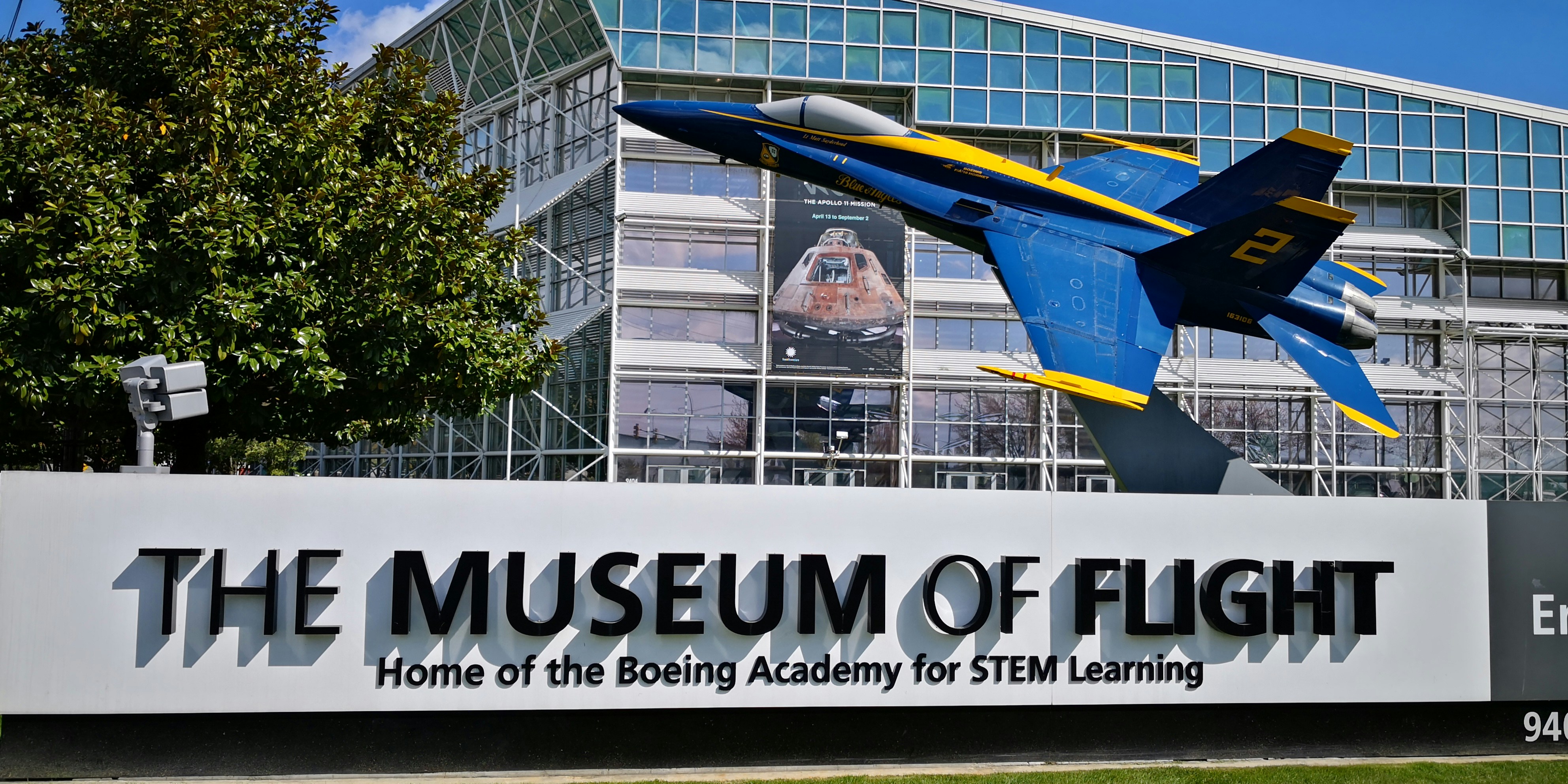 A blue and yellow fighter jet model prominently displayed above the entrance of The Museum of Flight, showcasing aviation history and STEM education.