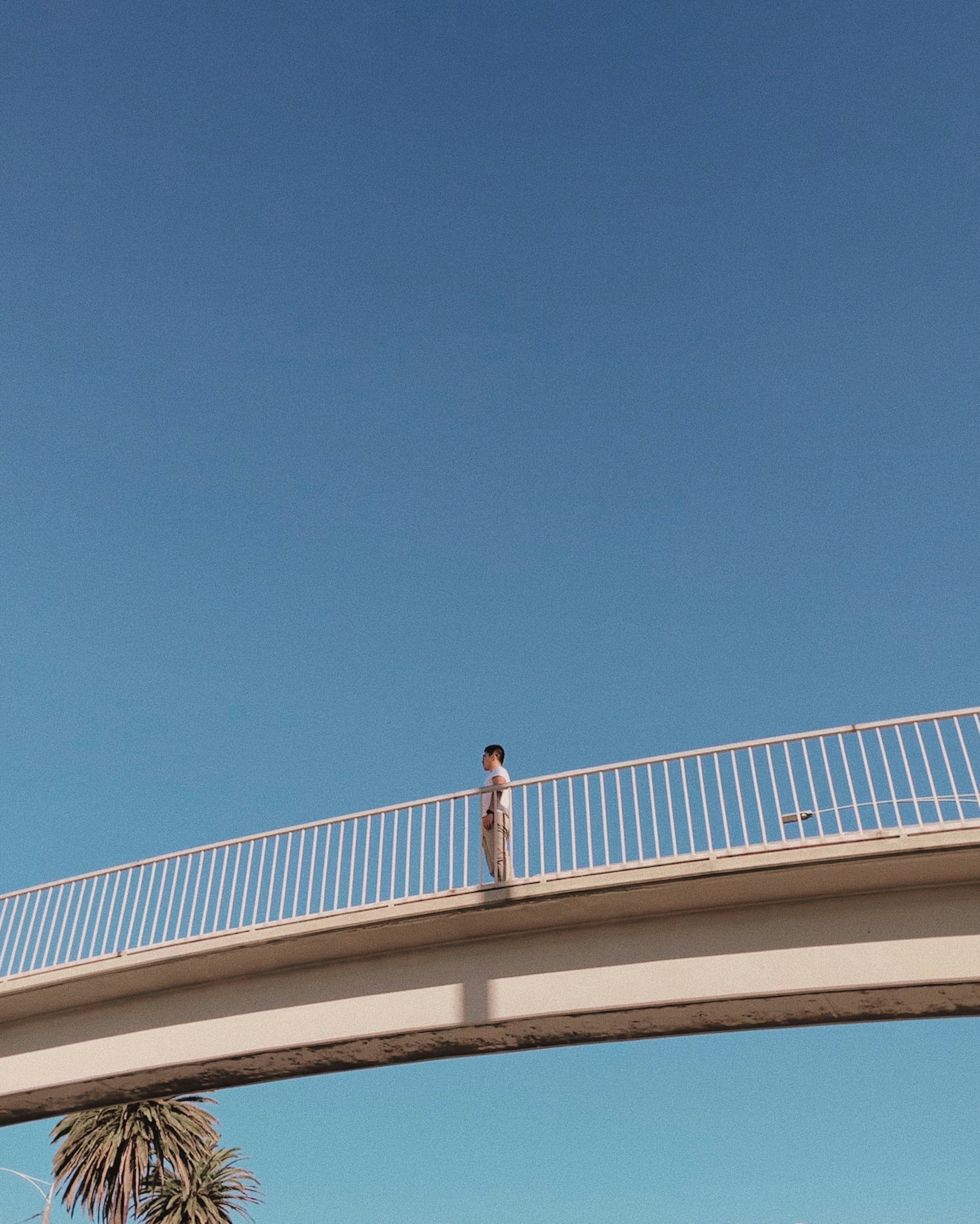 Arched Quiet: A solitary figure traverses a sunlit bridge beneath a boundless blue sky