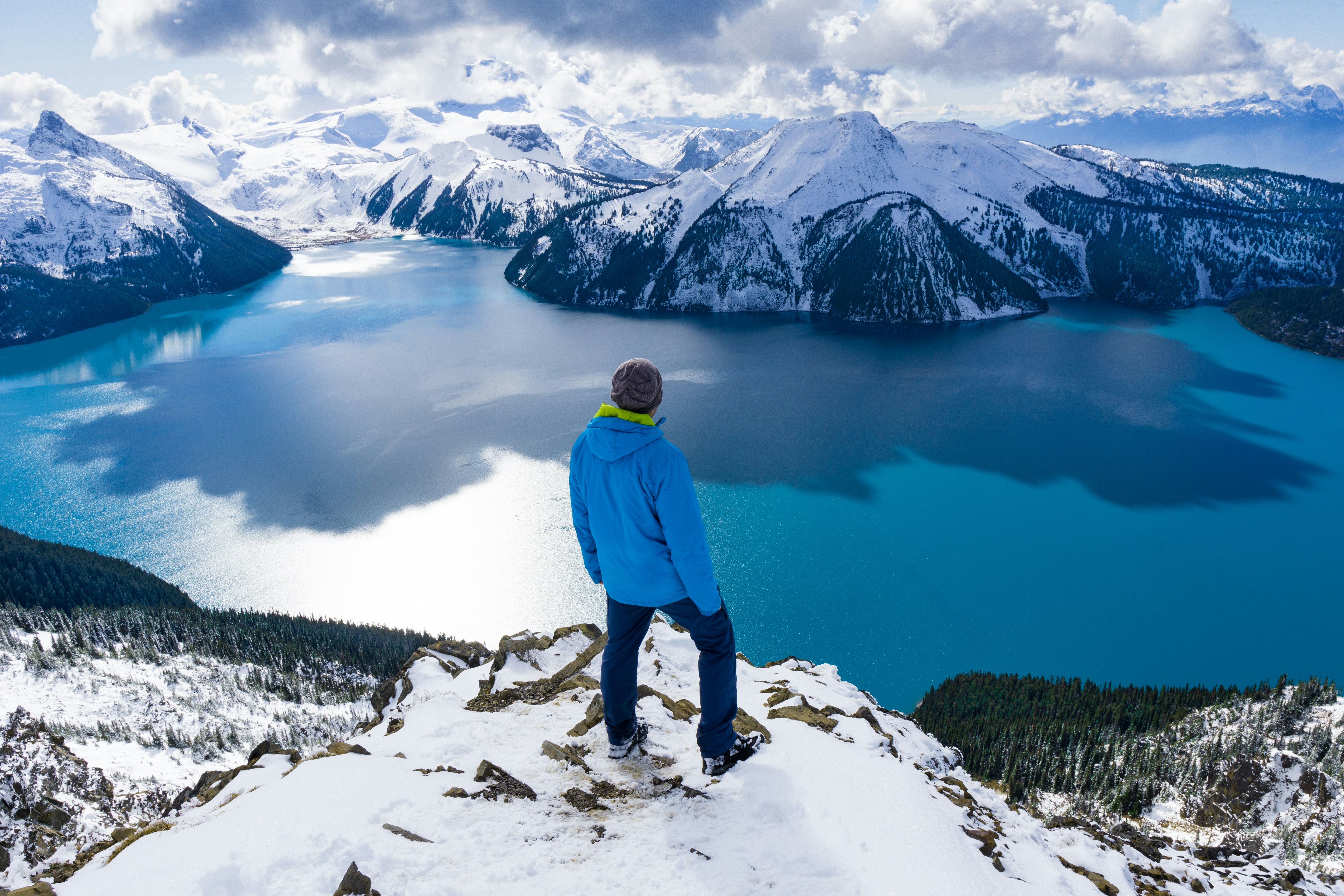 Edge of the World: A lone climber surveys a glacier-fed turquoise lake from a snow-dusted cliff