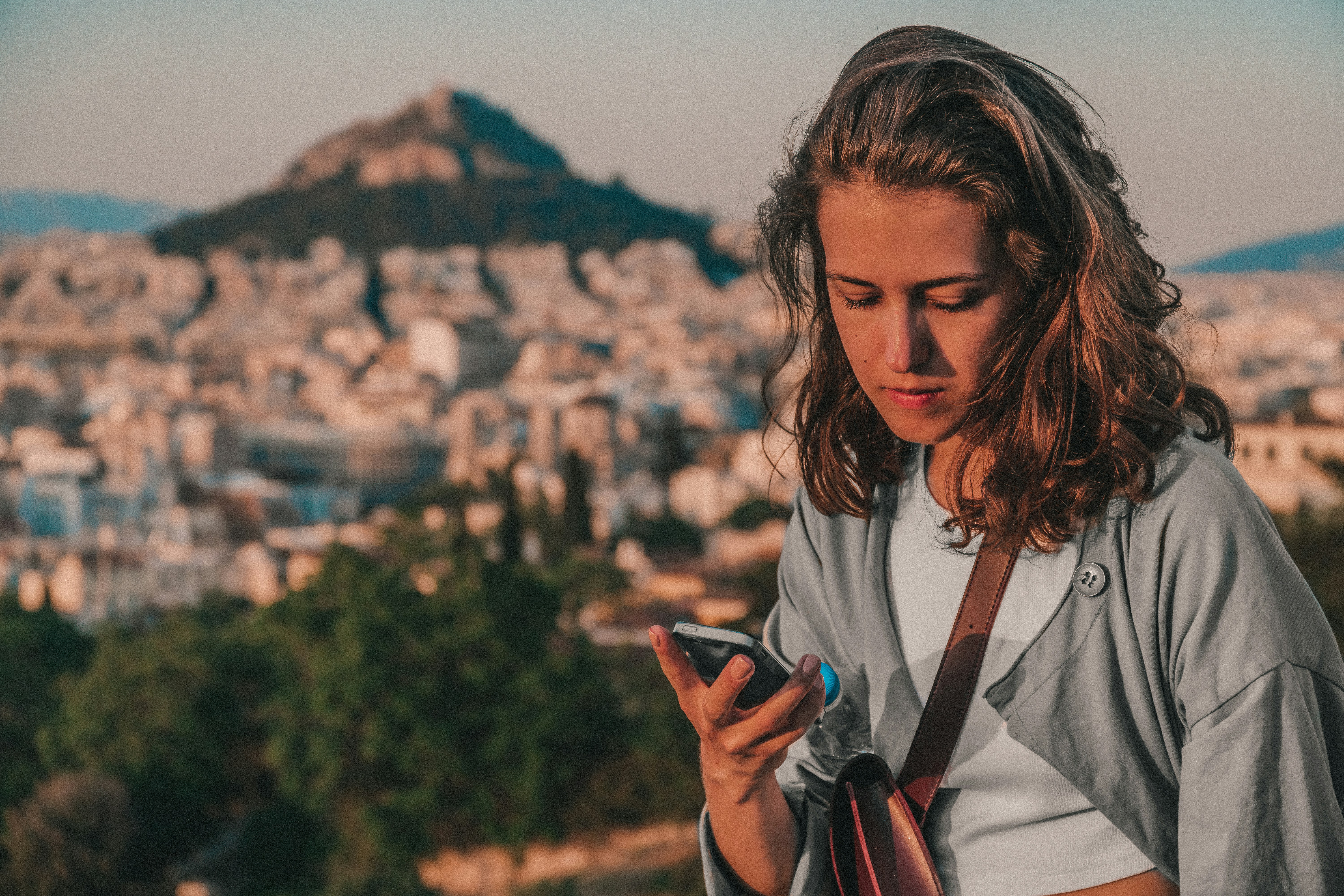 Golden Hour Glance: A Traveler Reads Her Phone Over a Sunlit Hilltown