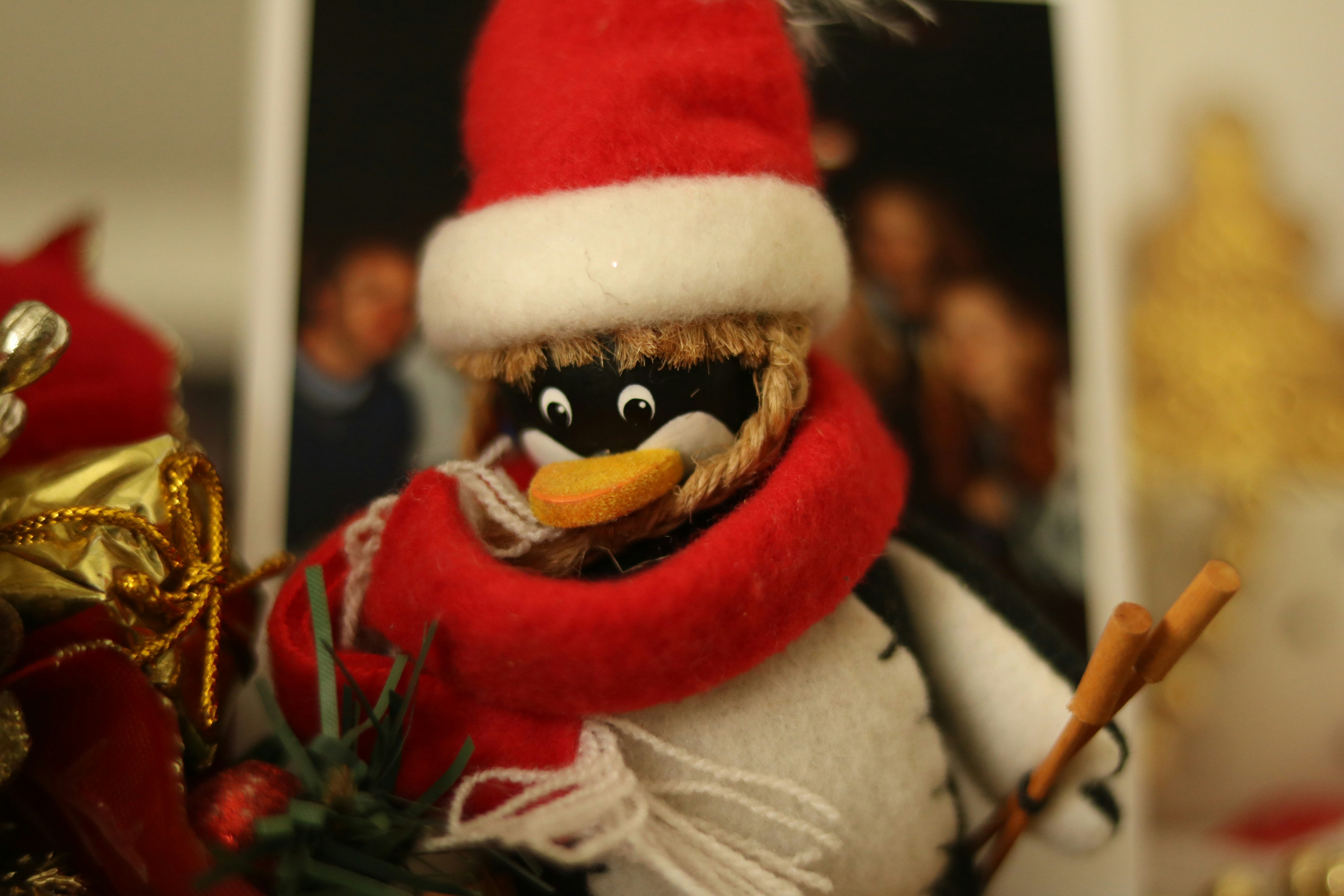 A whimsical penguin figurine adorned with a red scarf and hat, surrounded by holiday decorations. The cheerful expression adds to the festive atmosphere.