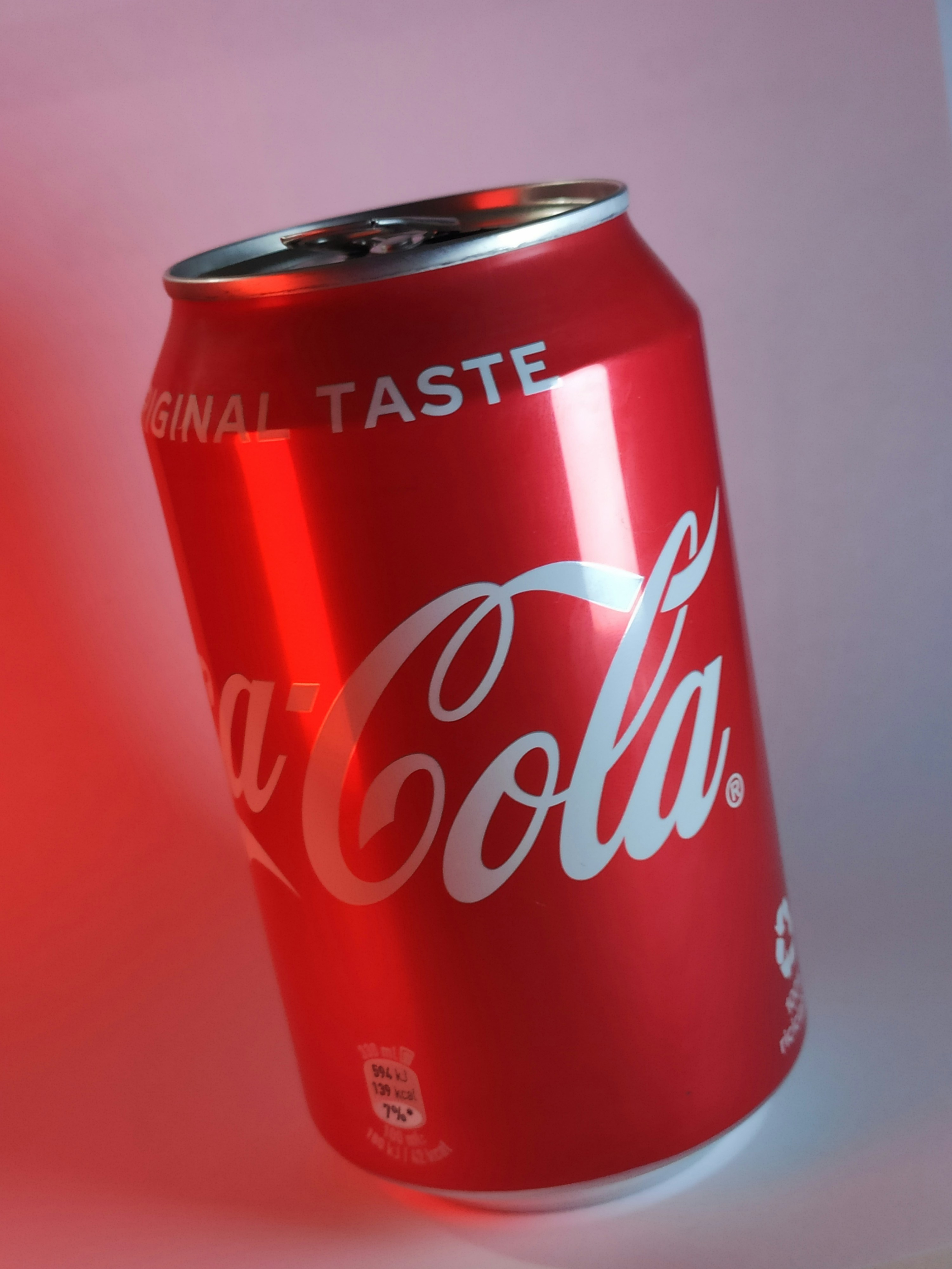 Close-up of a red Coca-Cola can tilted diagonally under pink lighting. The glossy surface and iconic script dominate the frame with a soft, moody backdrop.