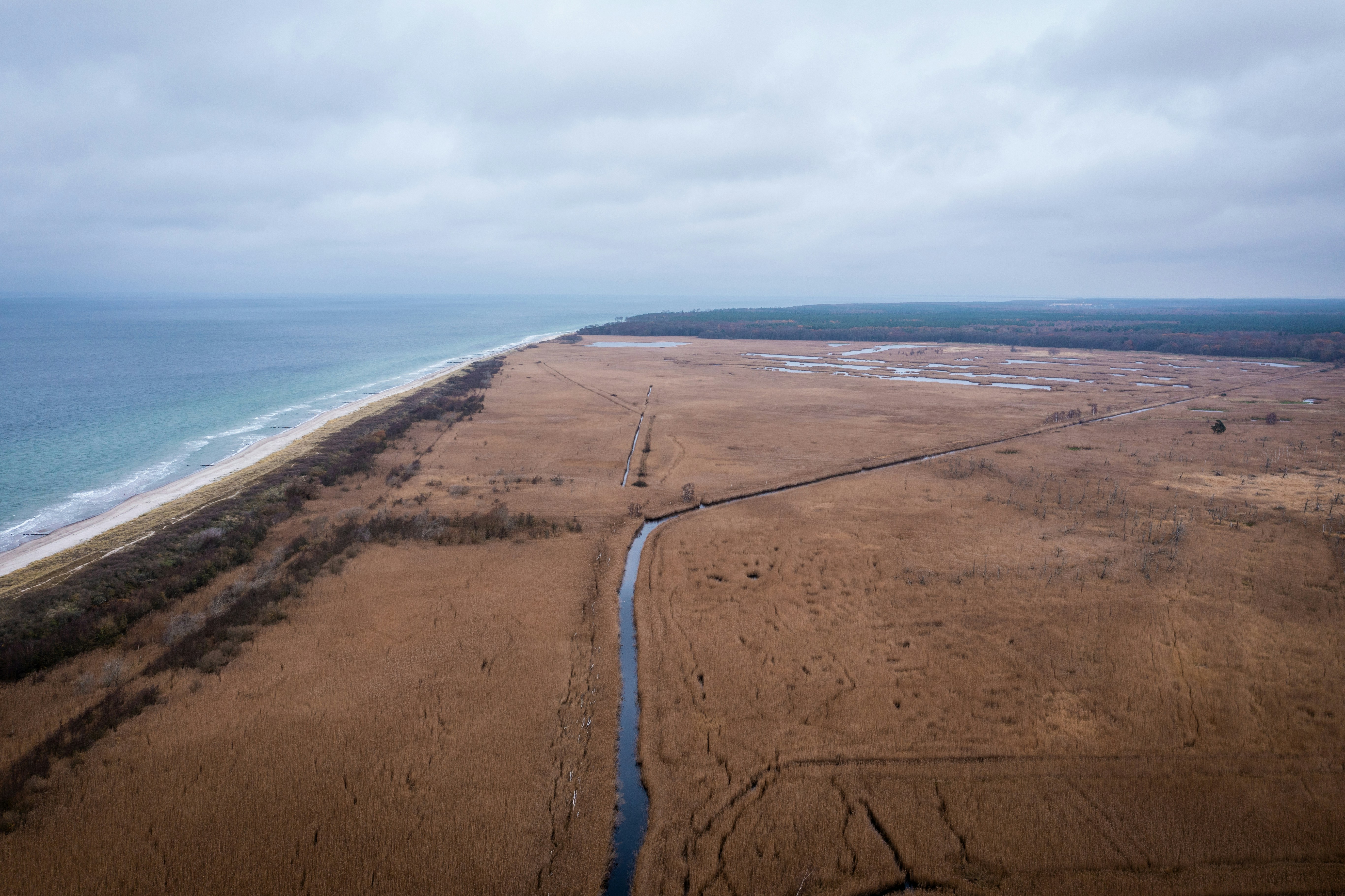Aerial view of a vast sandy coastline meeting the ocean under a cloudy sky.