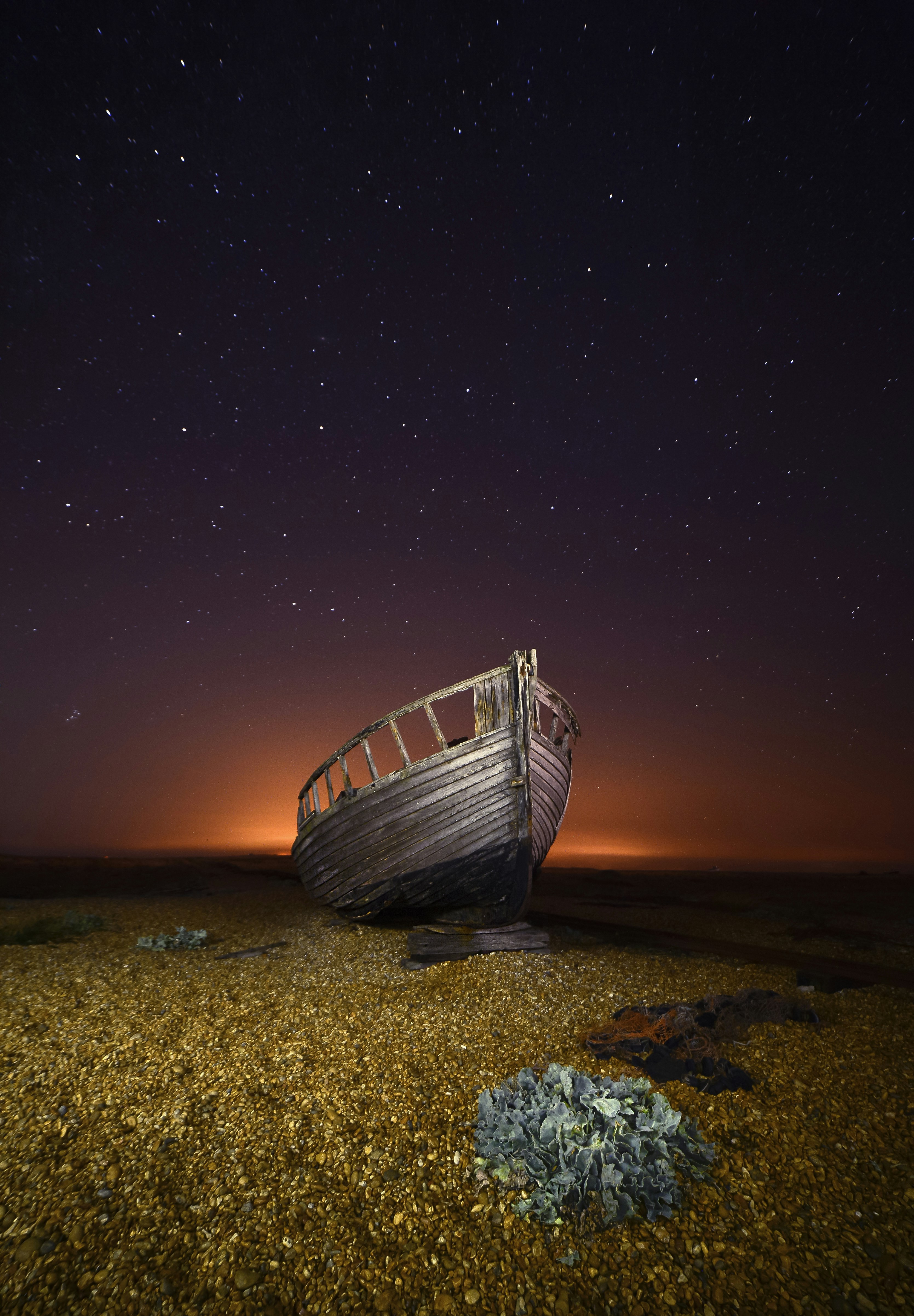 Old wooden boat on a starlit beach at night with a glowing horizon.