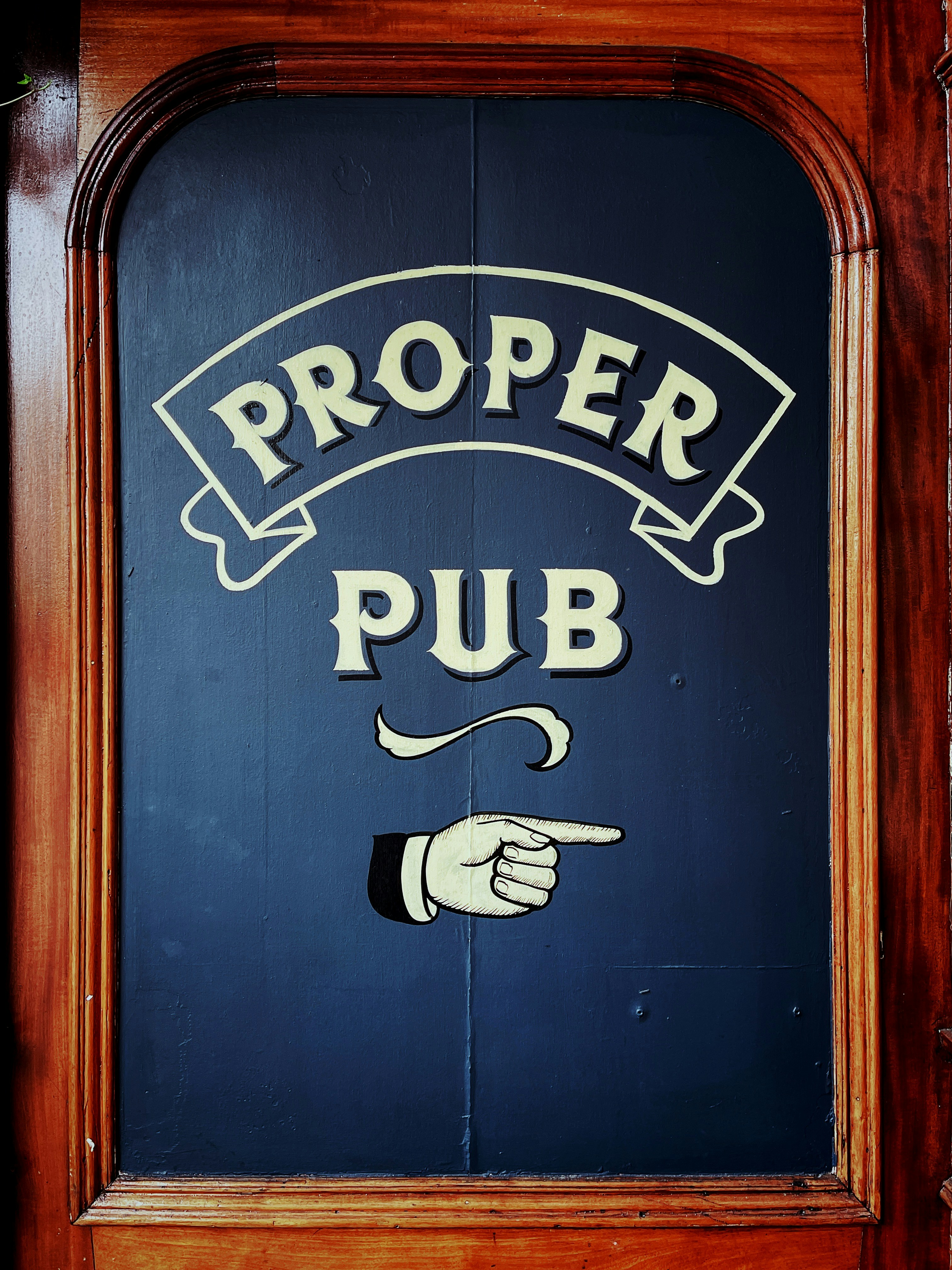Vintage pub sign featuring the words 'PROPER PUB' and an illustrated pointing hand. A blend of classic typography and design elements.