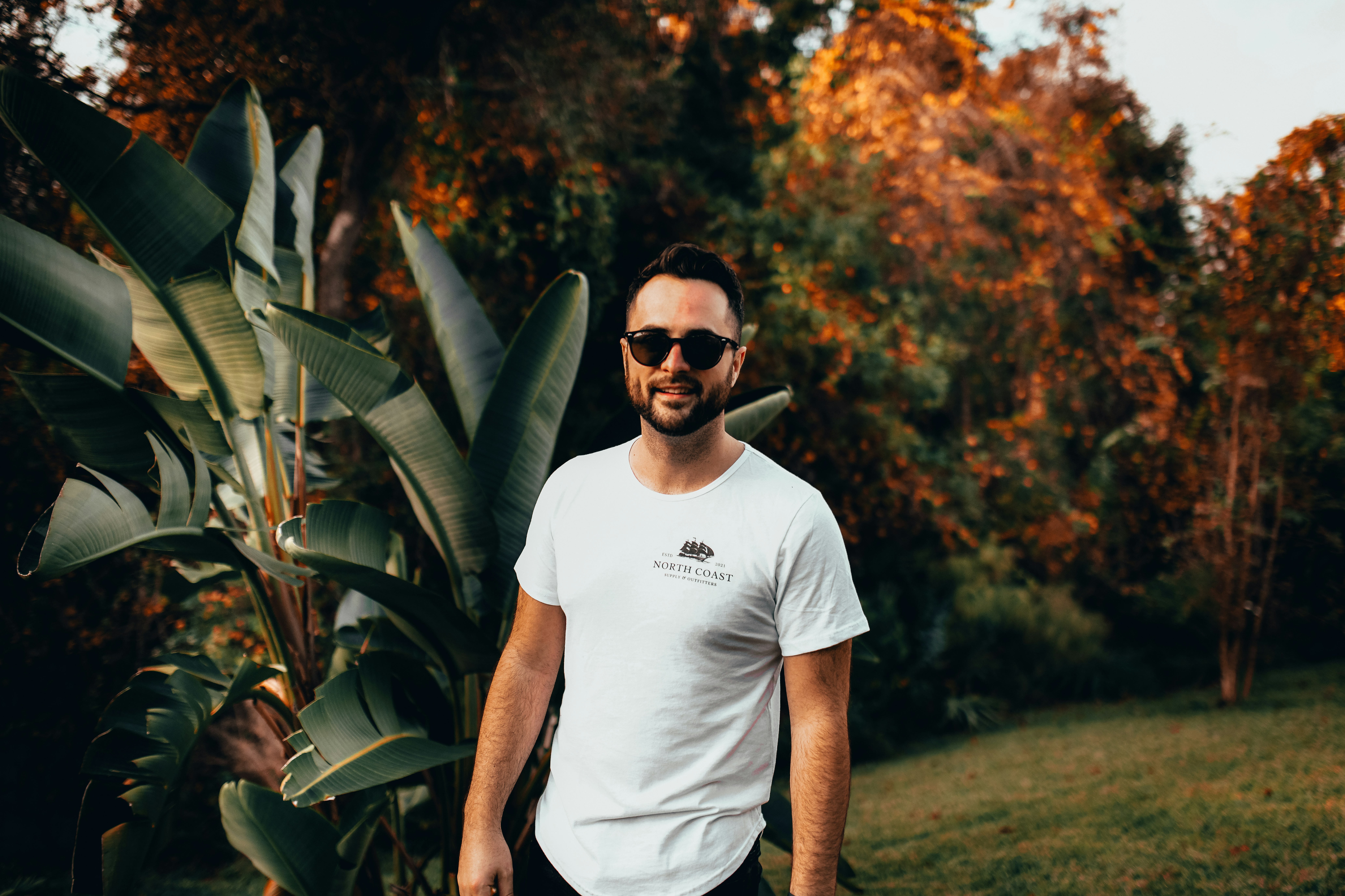 A man in a white shirt and sunglasses standing in front of a tree photo ...