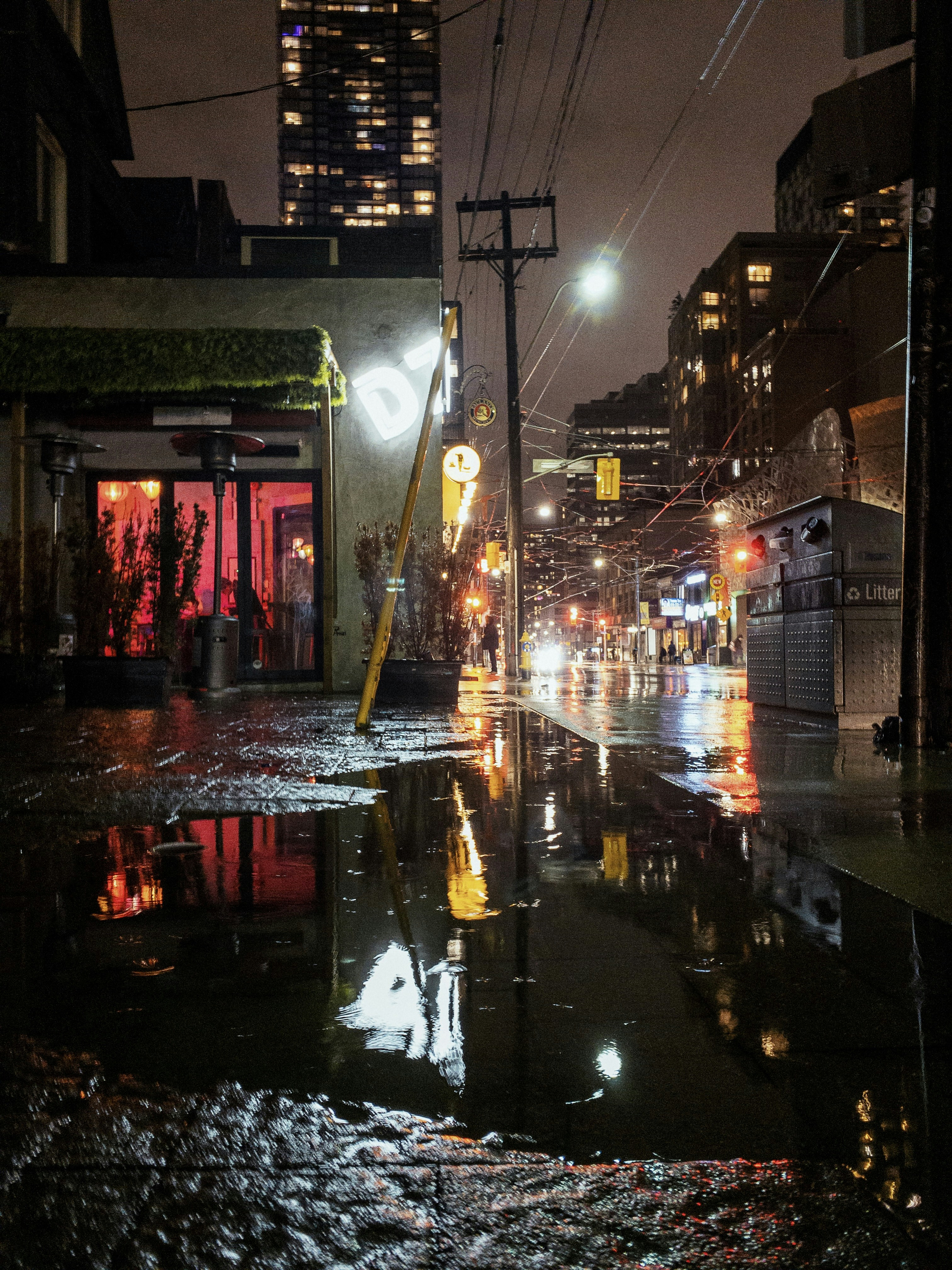 Vibrant reflections of city lights in puddles on a wet street at night, showcasing a lively urban atmosphere.