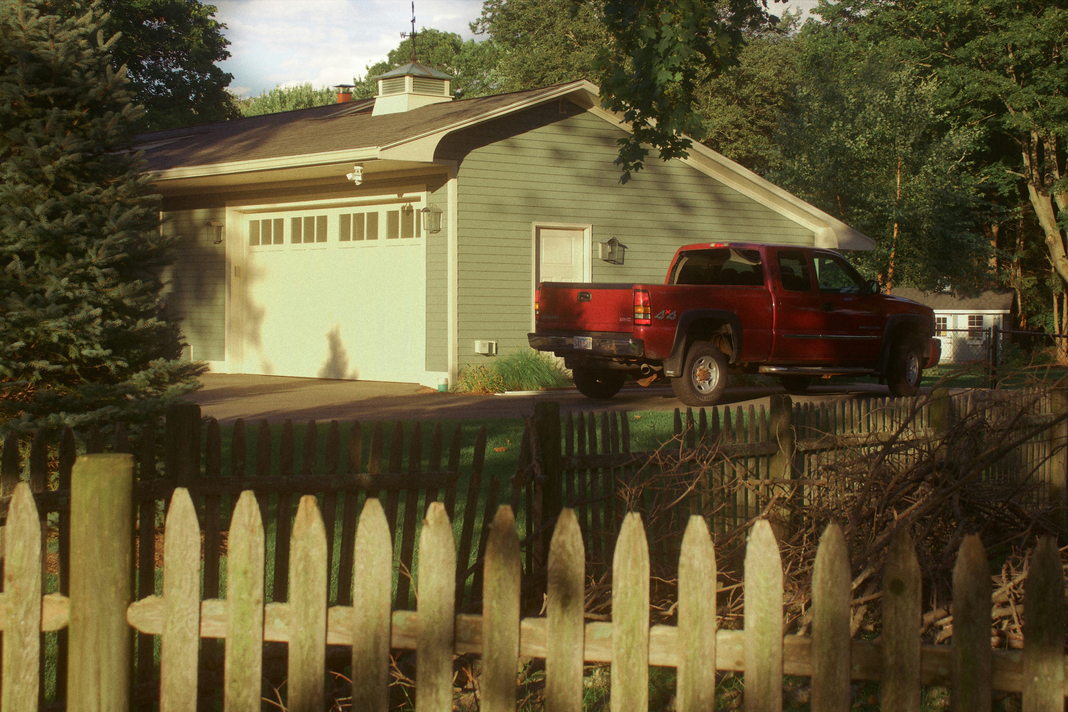 Red pickup tucked along a sunlit driveway in front of a green ranch-style home