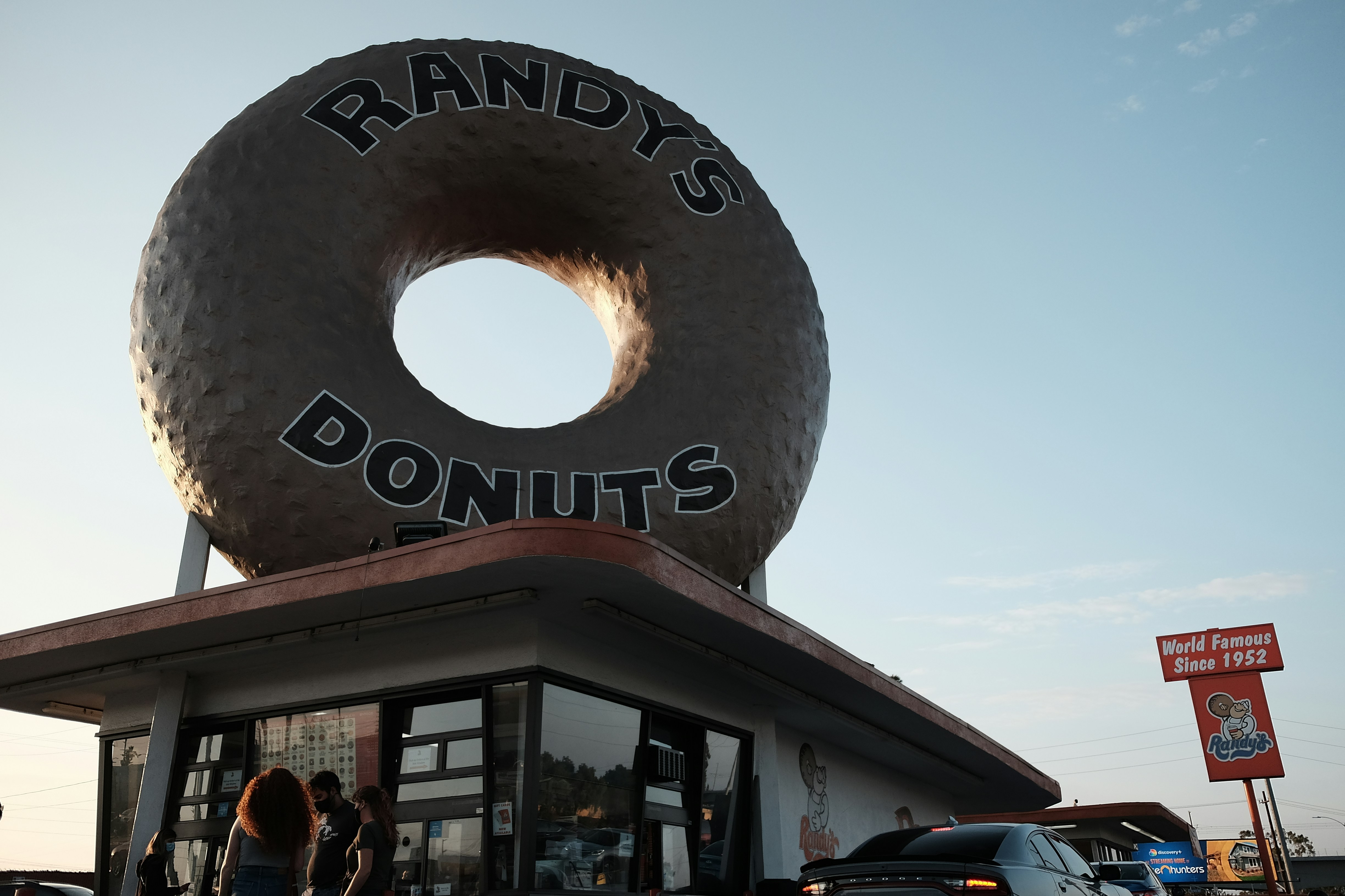 Giant donut sculpture perched atop a donut shop at sunset.