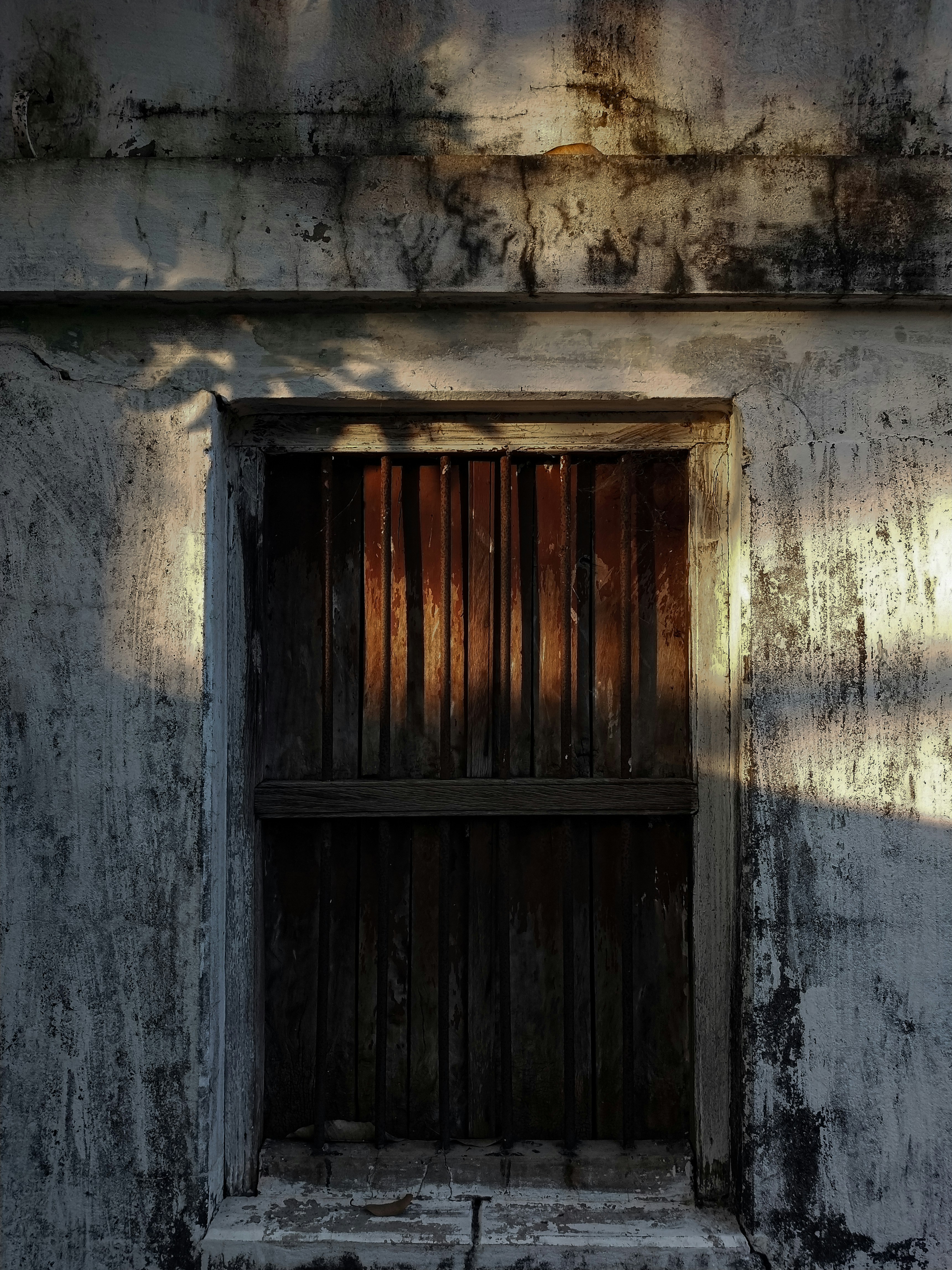 Weathered wooden shutters framed by peeling paint and soft light, evoking a sense of nostalgia and quiet decay.