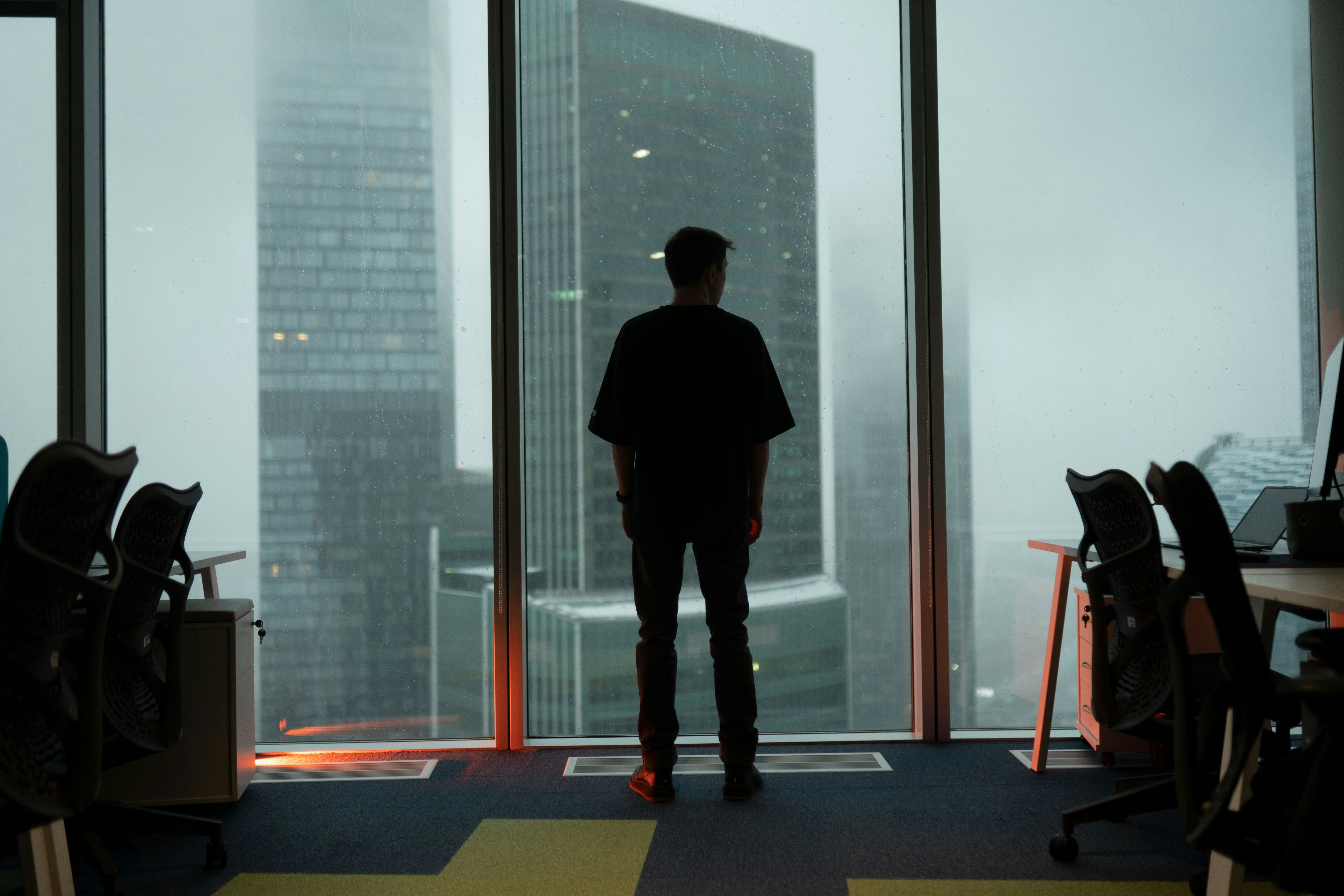 A man standing in an office looking out the window photo – Free City ...