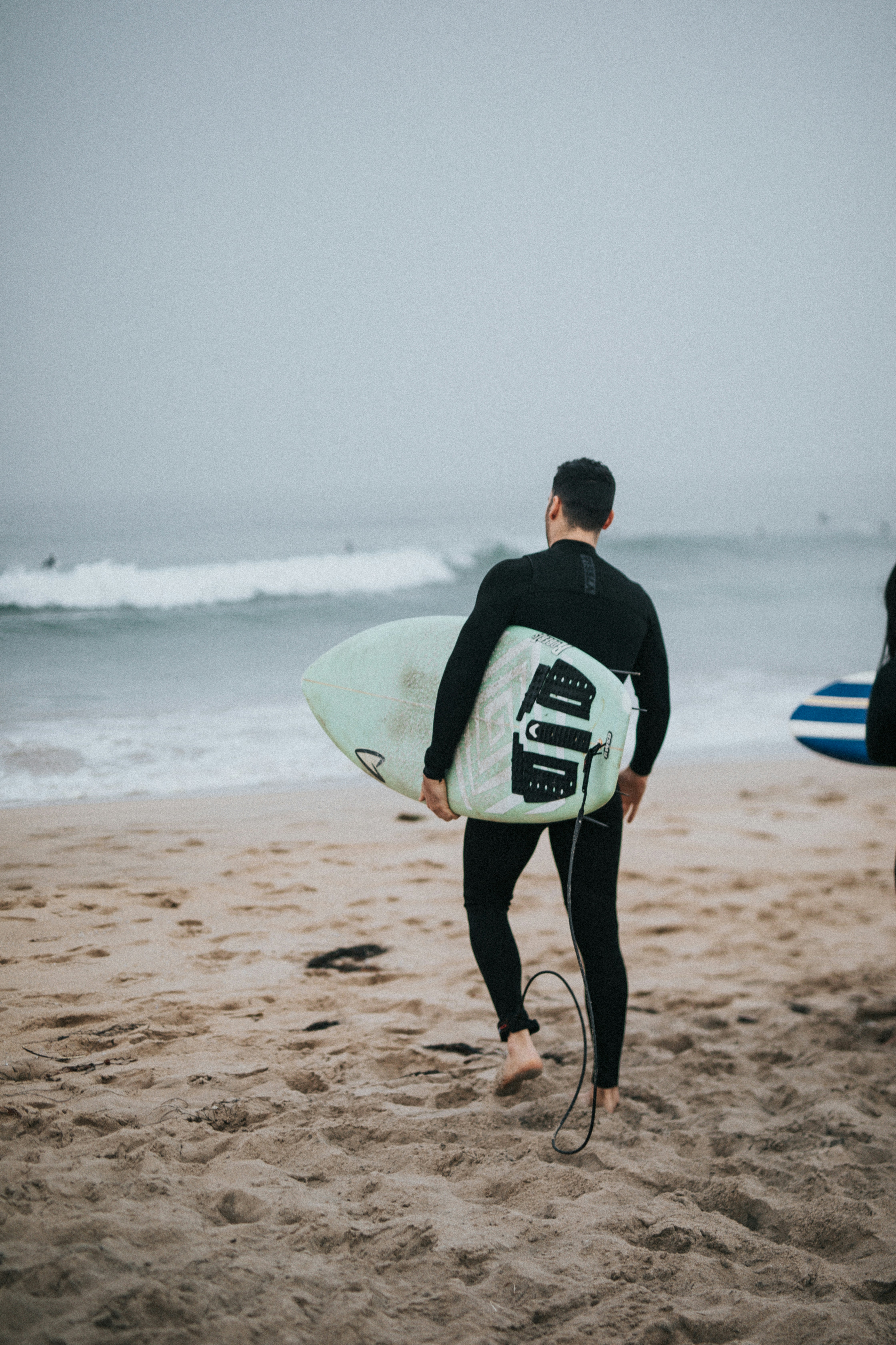 Mintboard Momentum: A Surfer Heads Toward the Break on a Quiet Shore