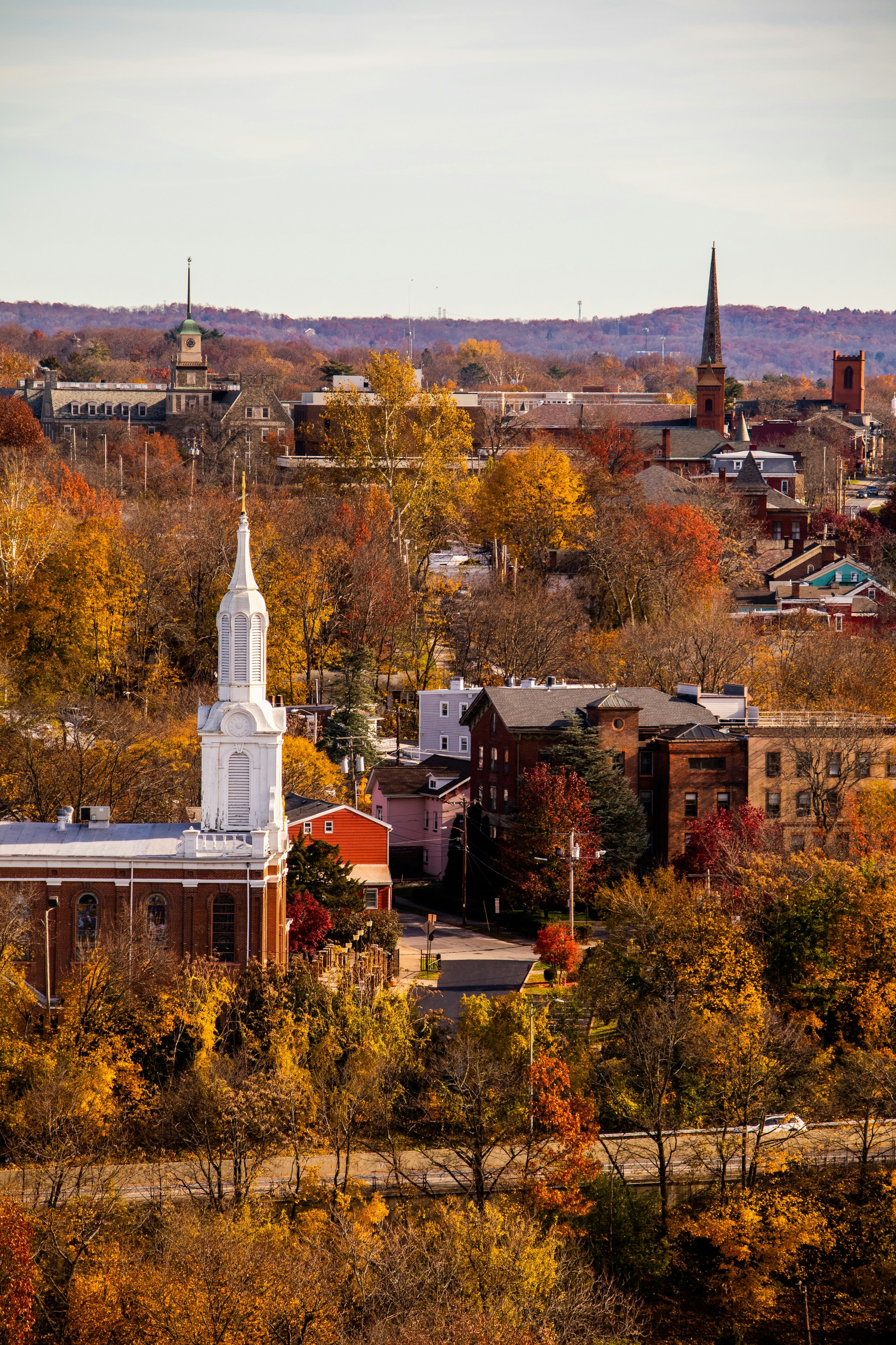 Aerial view of a quaint town with vibrant fall foliage and a prominent white church steeple.