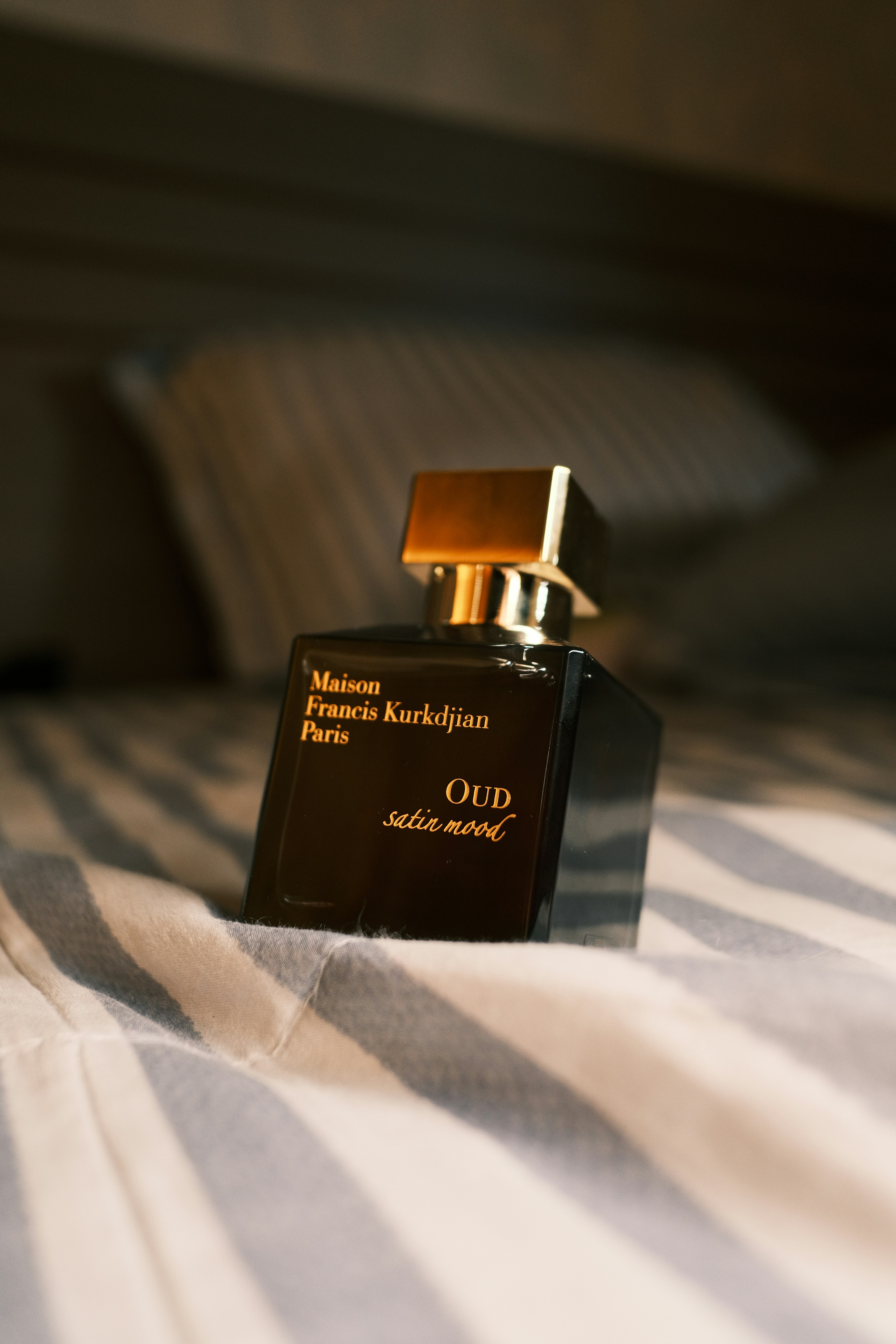 Luxurious perfume bottle resting on a softly striped bedspread, highlighting its sleek design and rich branding.