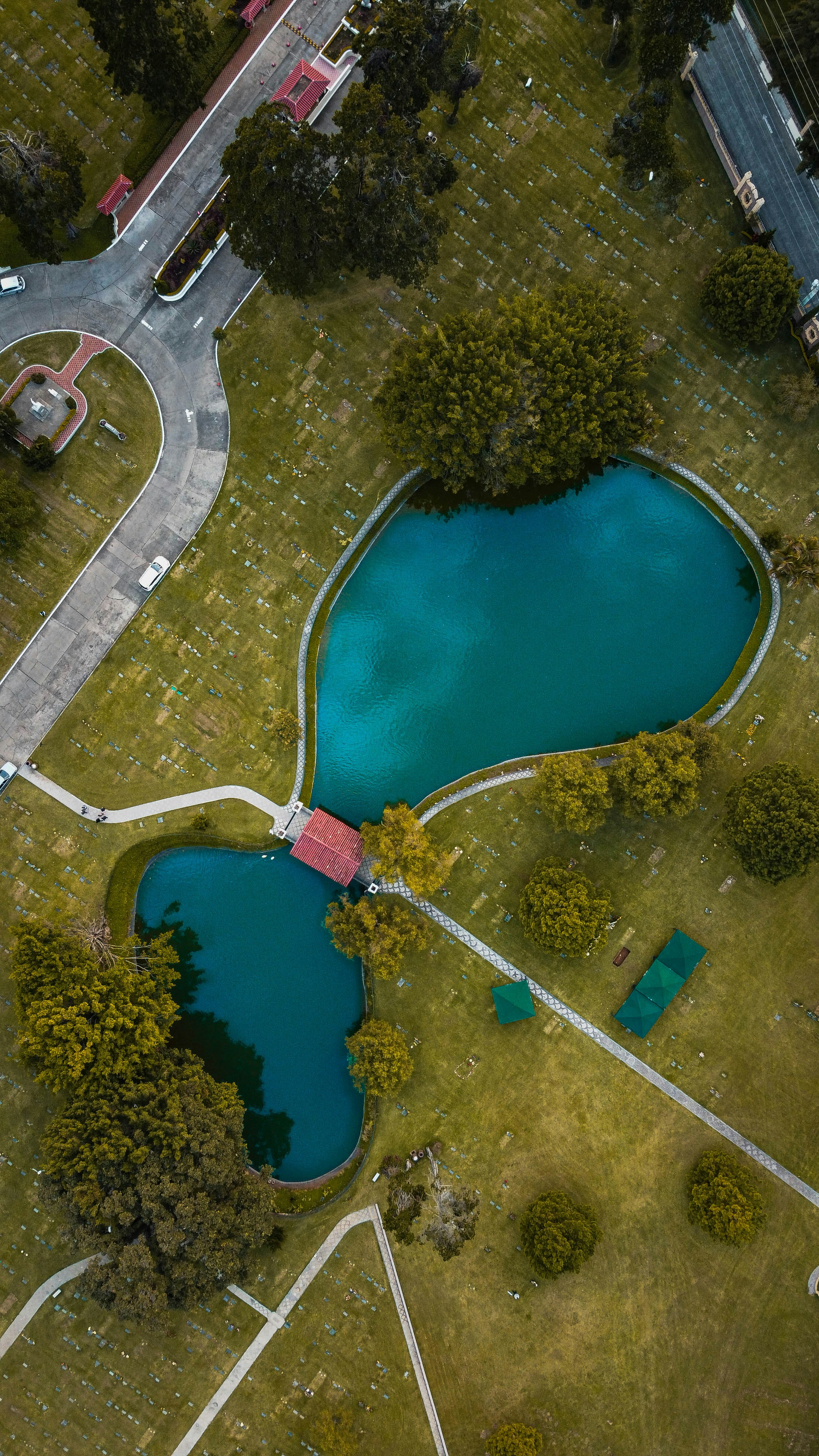 Aerial view of two interconnected ponds surrounded by lush greenery and pathways, highlighting the tranquility of the landscape within a cemetery.