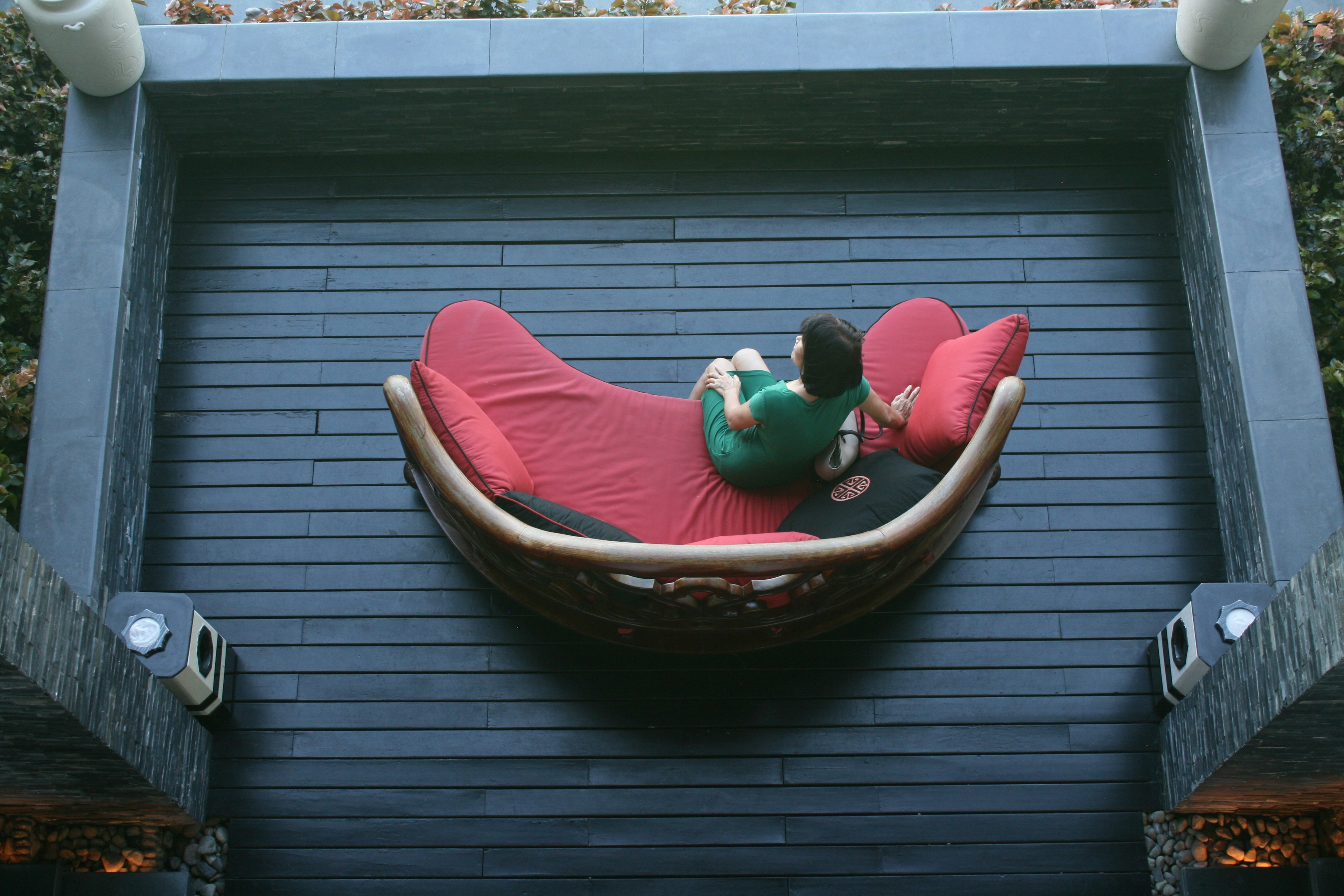 Aerial View: Person Reclining on a Red Canopy Sofa Amid Dark Decking