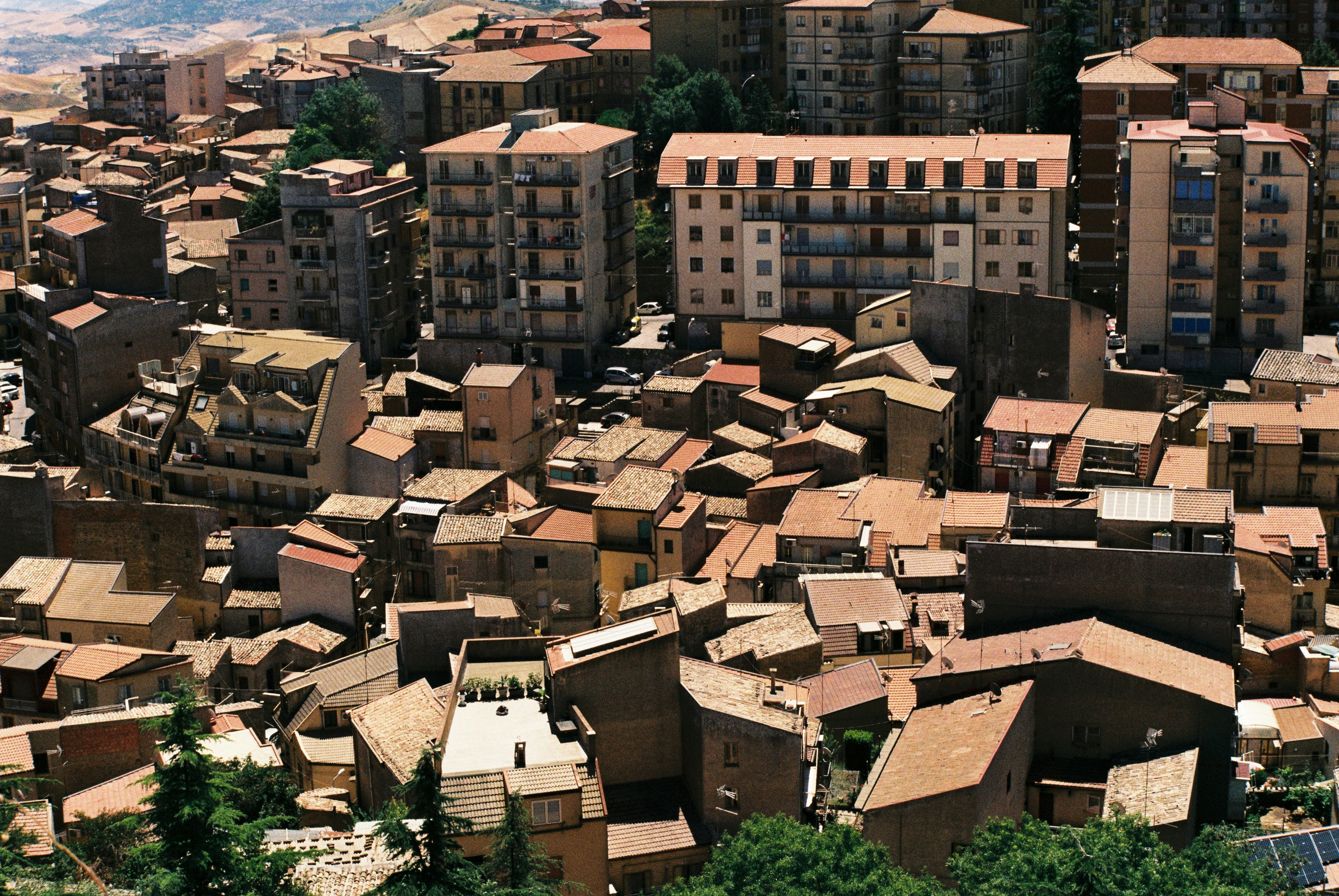 Aerial view of a densely packed urban landscape showcasing a variety of terracotta rooftops and multi-story buildings nestled among the hills.