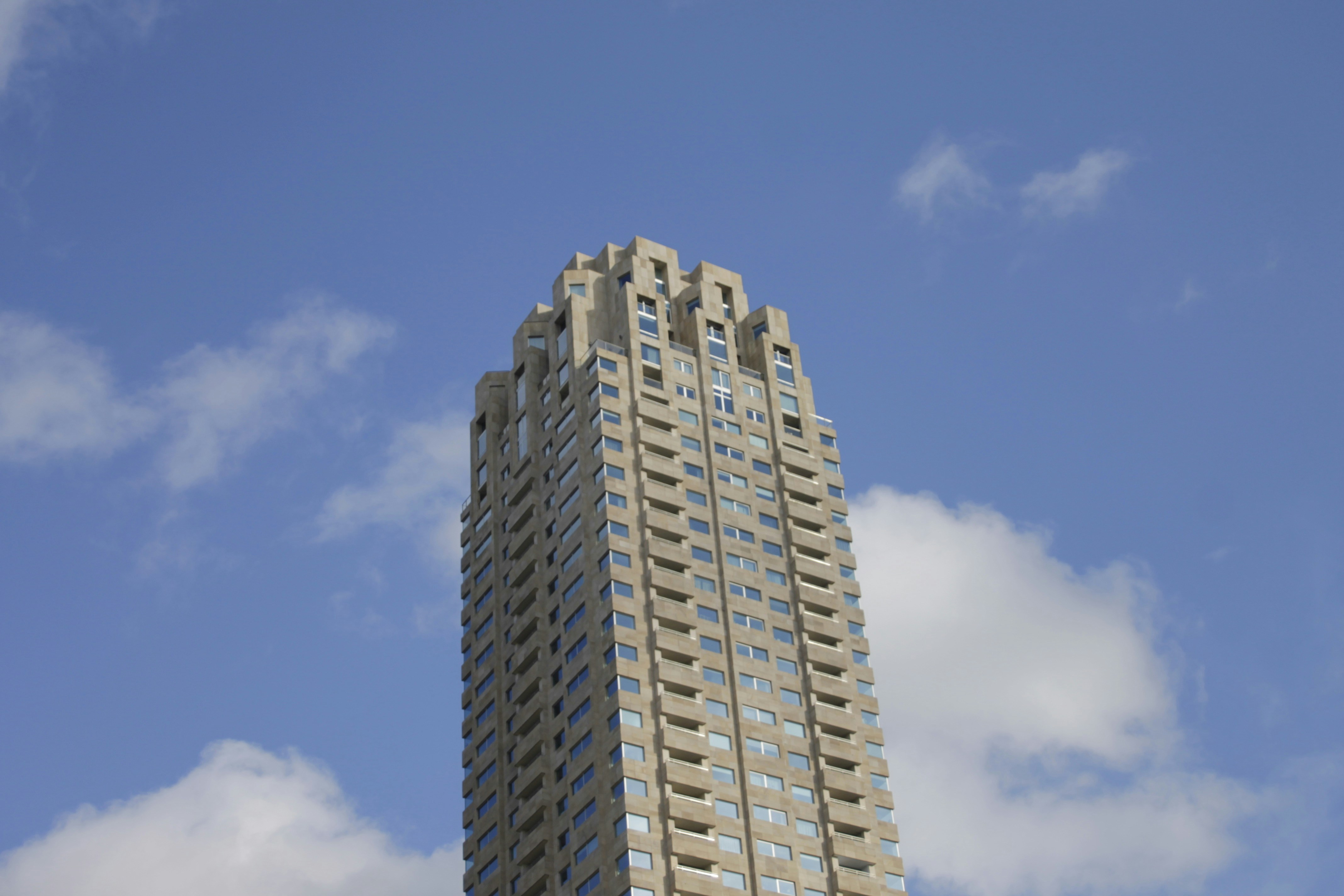 A towering residential skyscraper reaches for the sky, framed by a backdrop of wispy clouds and blue expanse.
