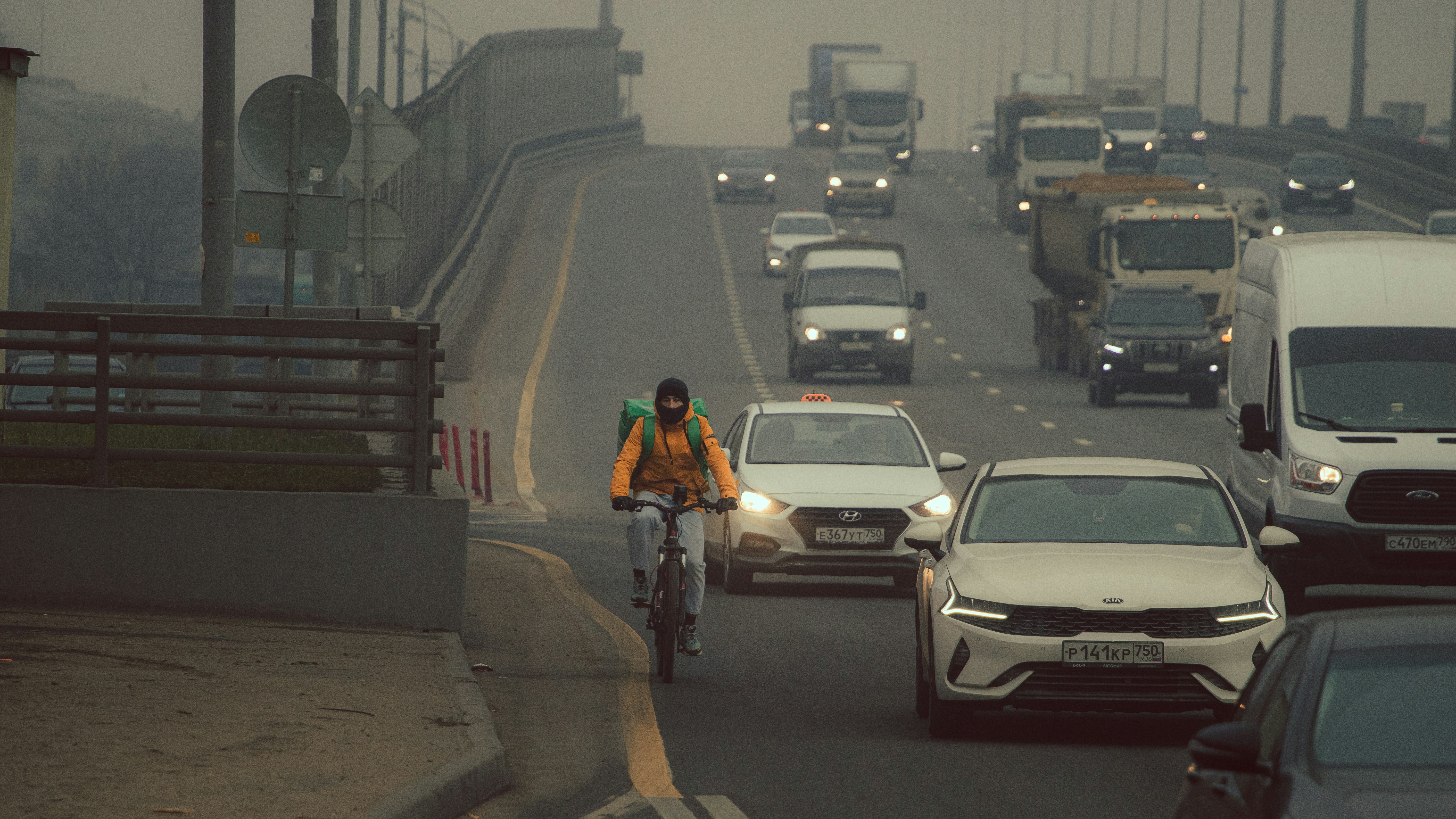 Orange Pulse on a Fogged Bridge: Cyclist Navigates Morning Traffic