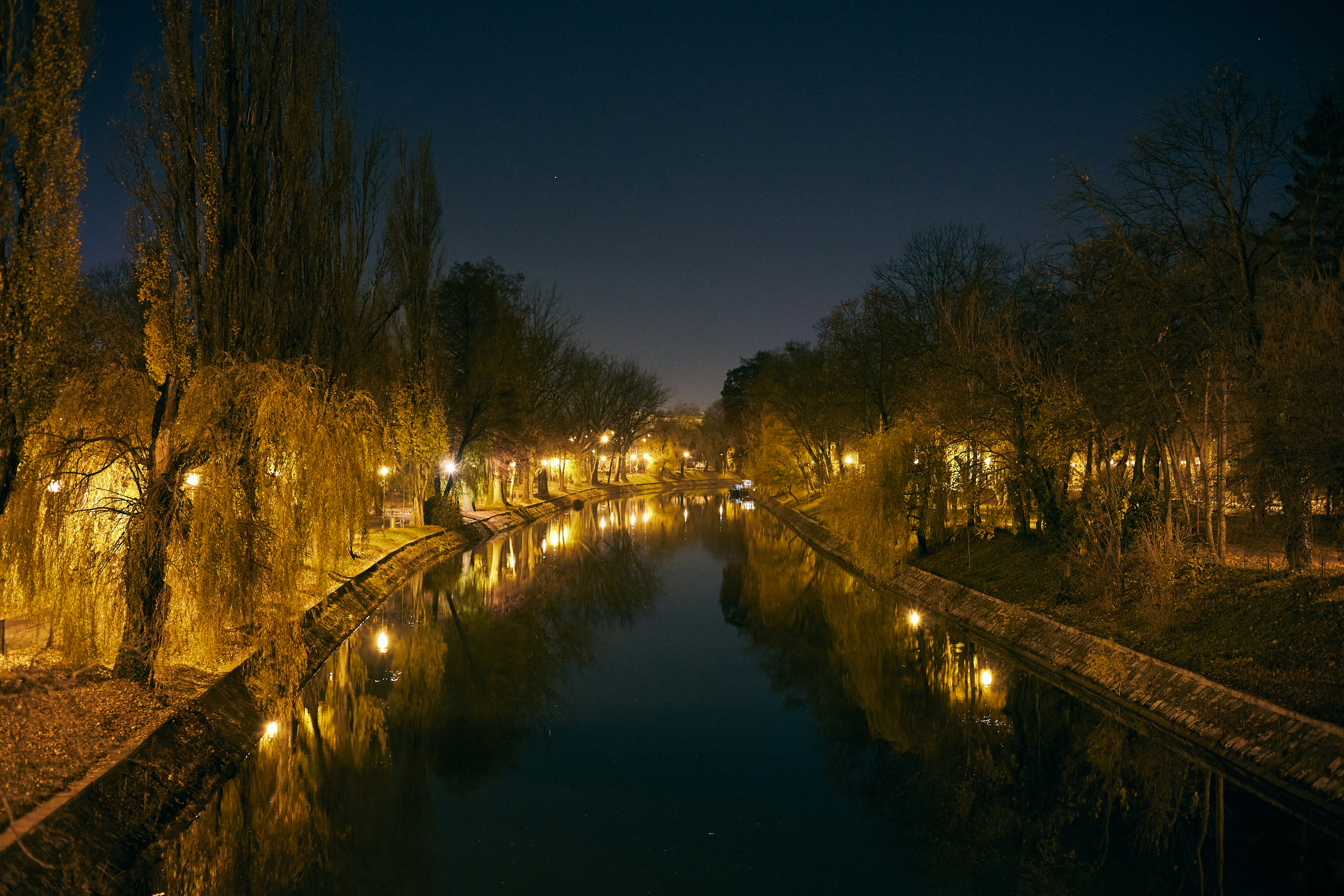 Serene nighttime view of a calm river flanked by softly lit trees and distant buildings.