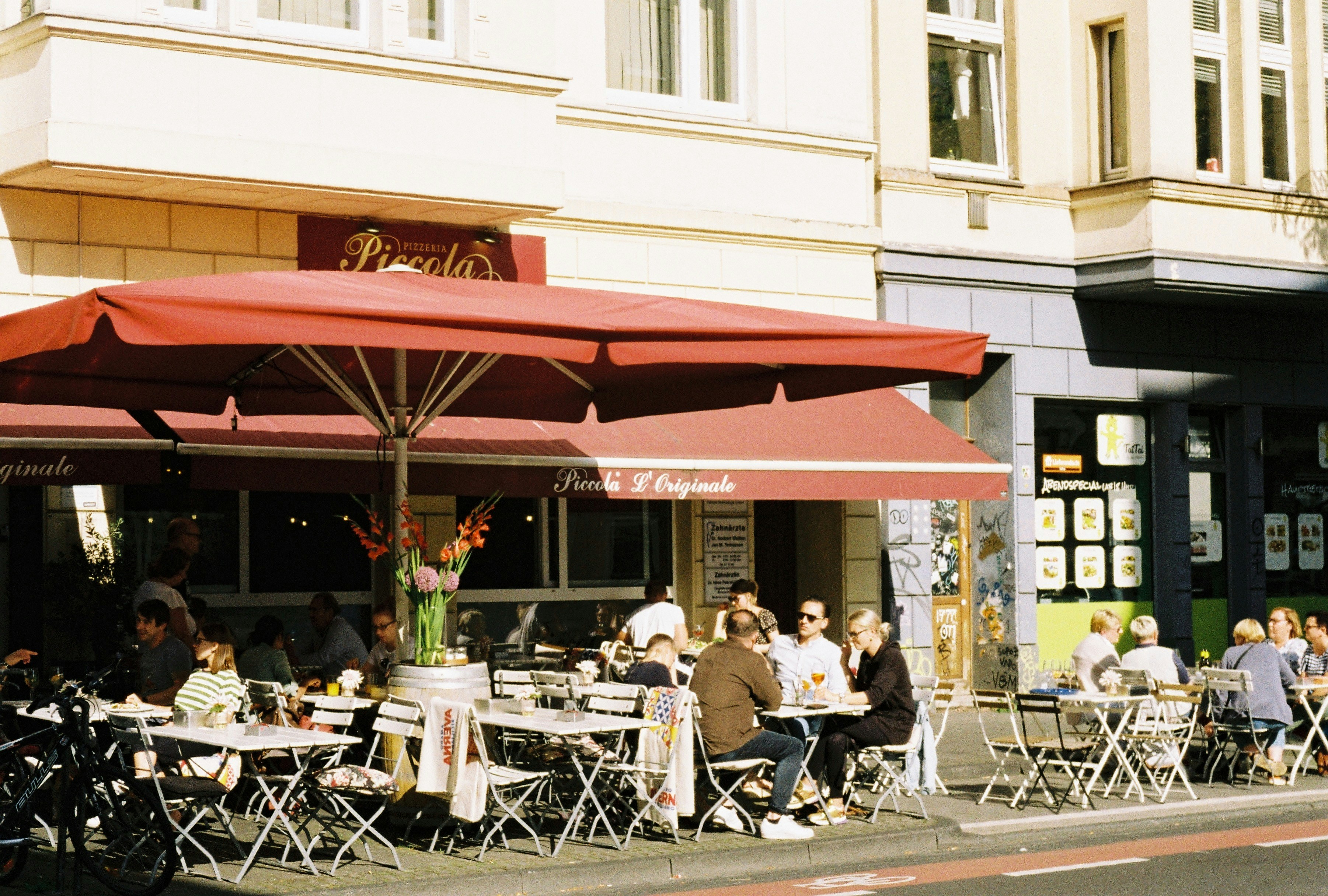 A group of people sitting at tables under a red umbrella photo – Free ...