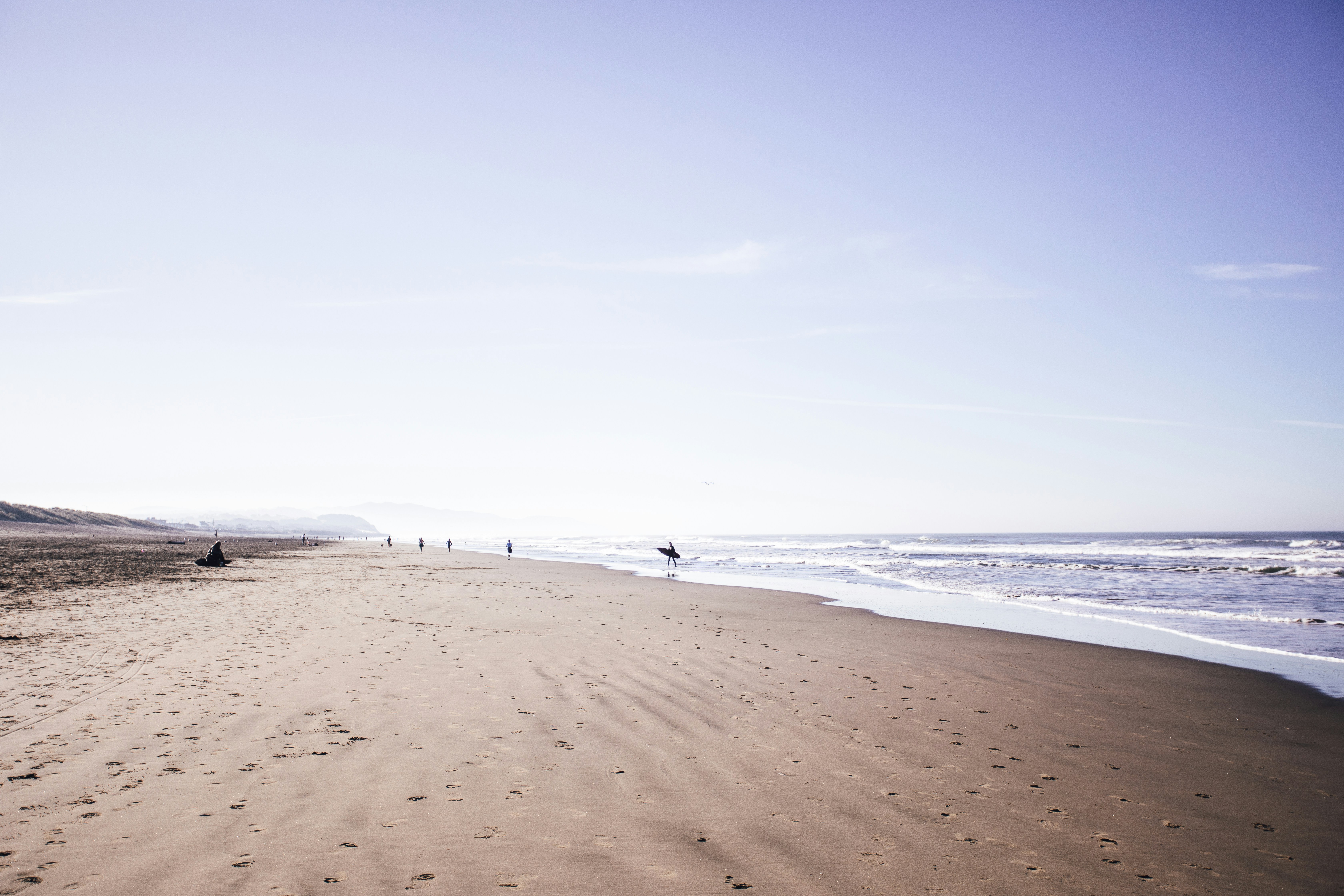 A serene beach scene featuring distant figures walking along the shore, with gentle waves lapping at the sand under a clear sky.