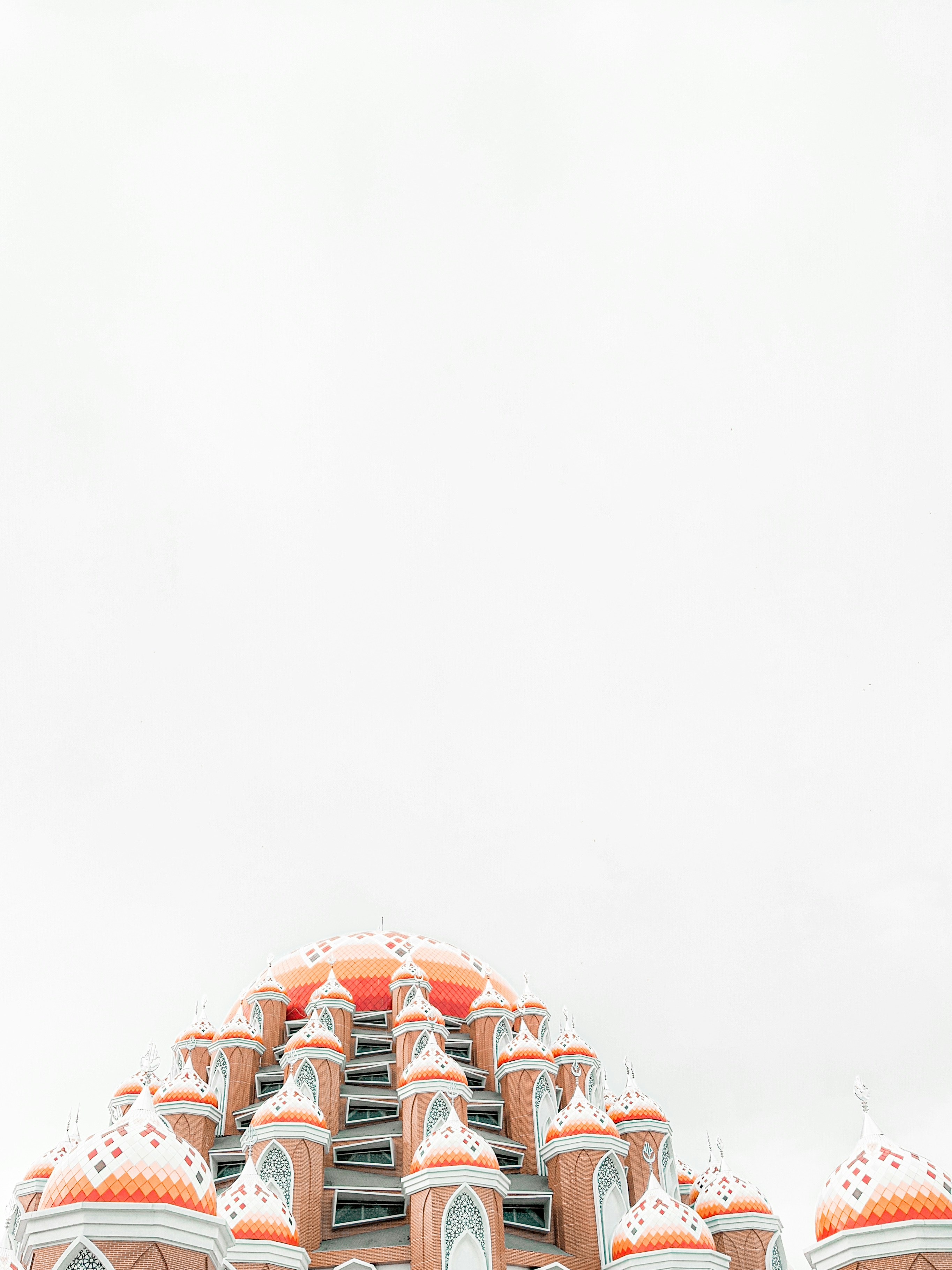 Architectural photograph of ornate orange-domed spires atop a tall brick tower set against a pale sky.