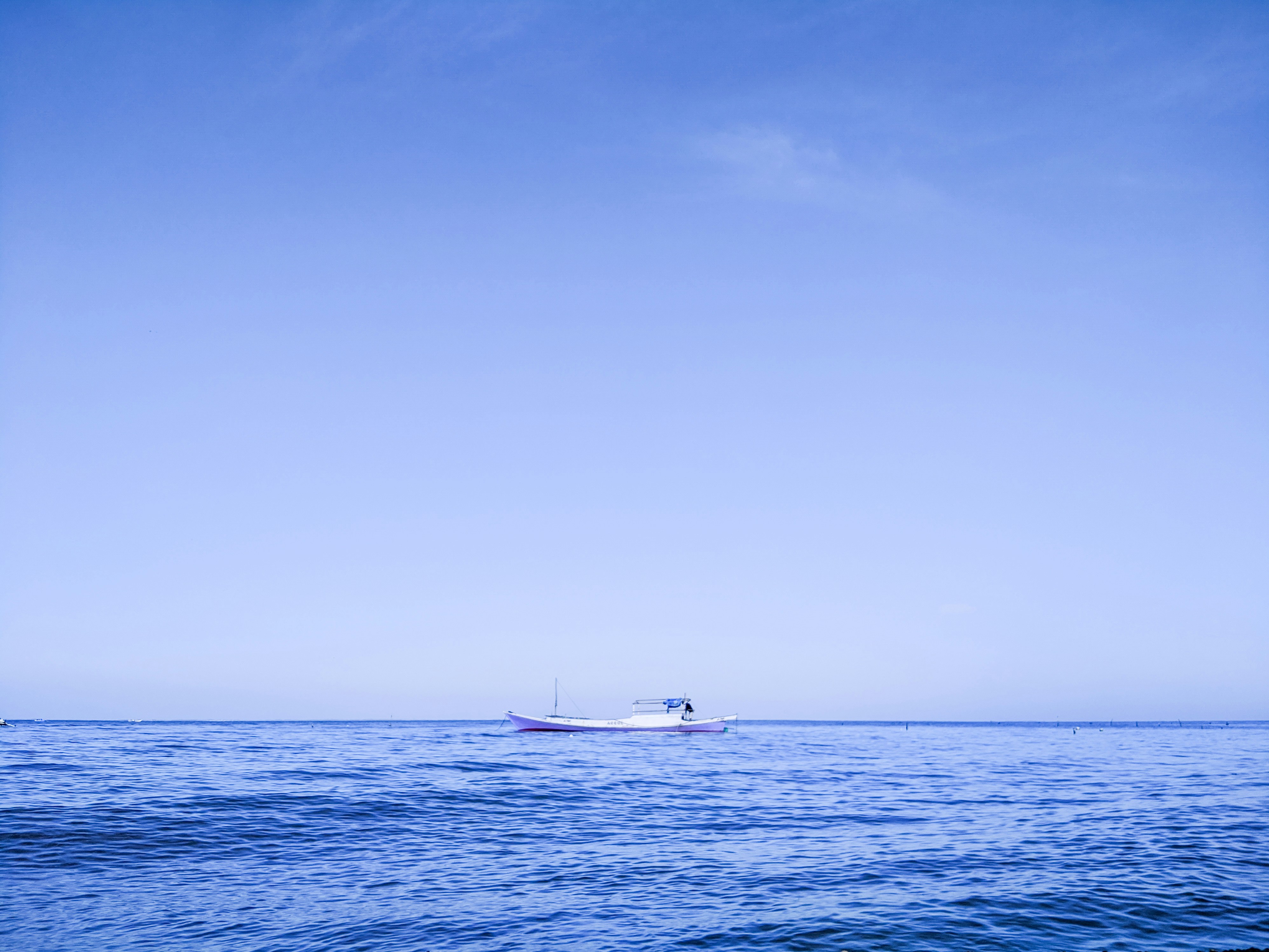 A lone boat glides across a tranquil sea under a soft blue sky, evoking a sense of peace and solitude.