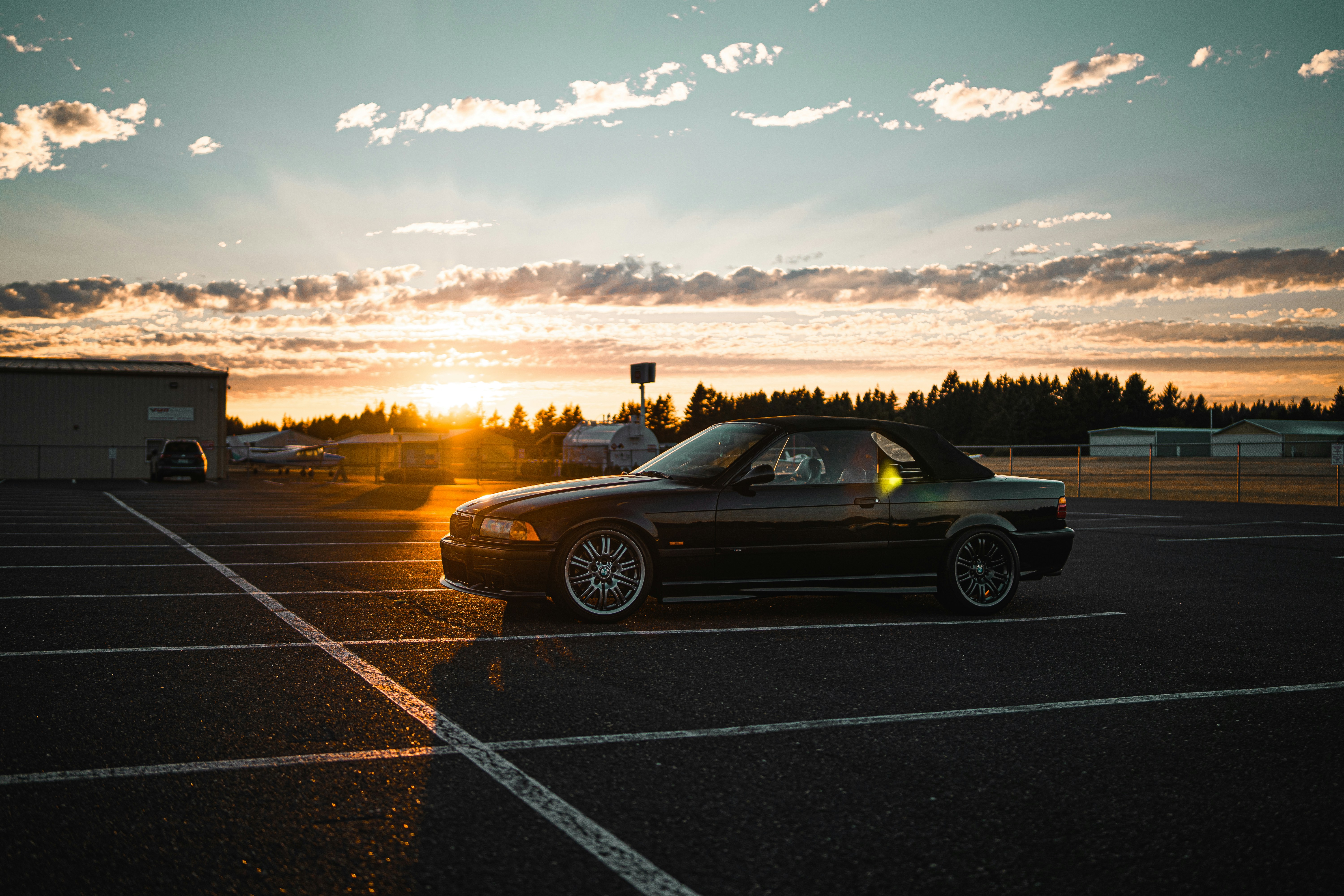 Classic car parked in an empty lot during sunset, with vibrant colors illuminating the scene.